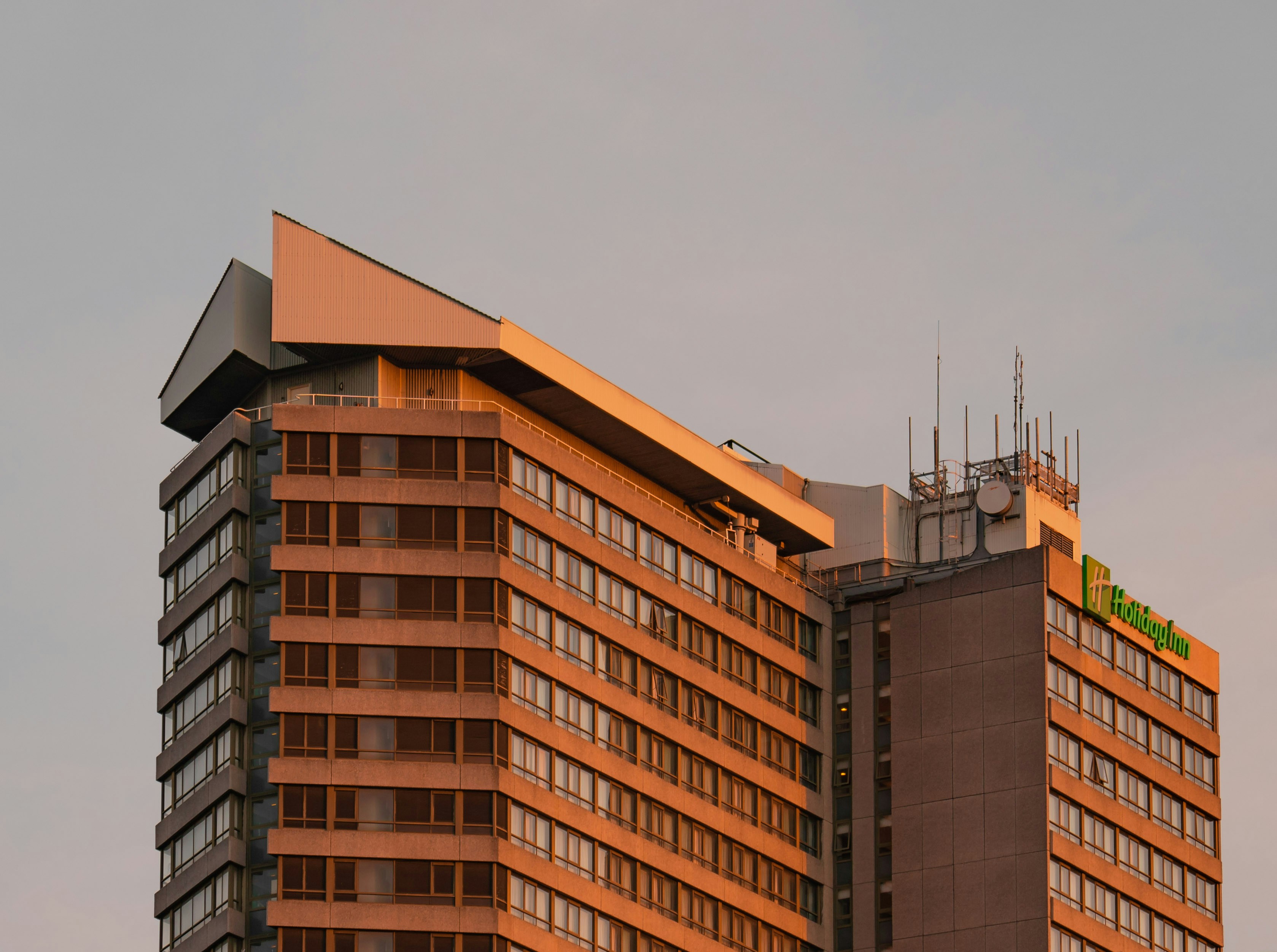 The upper section of a contemporary hotel building, showcasing angular design and a mix of materials against a soft evening sky.