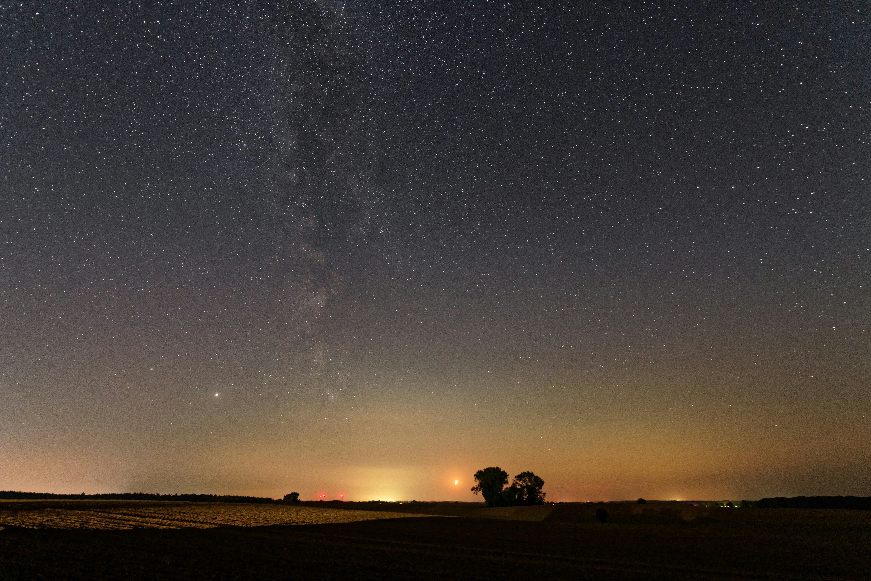 Star-filled night sky with the Milky Way above a dark rural landscape.
