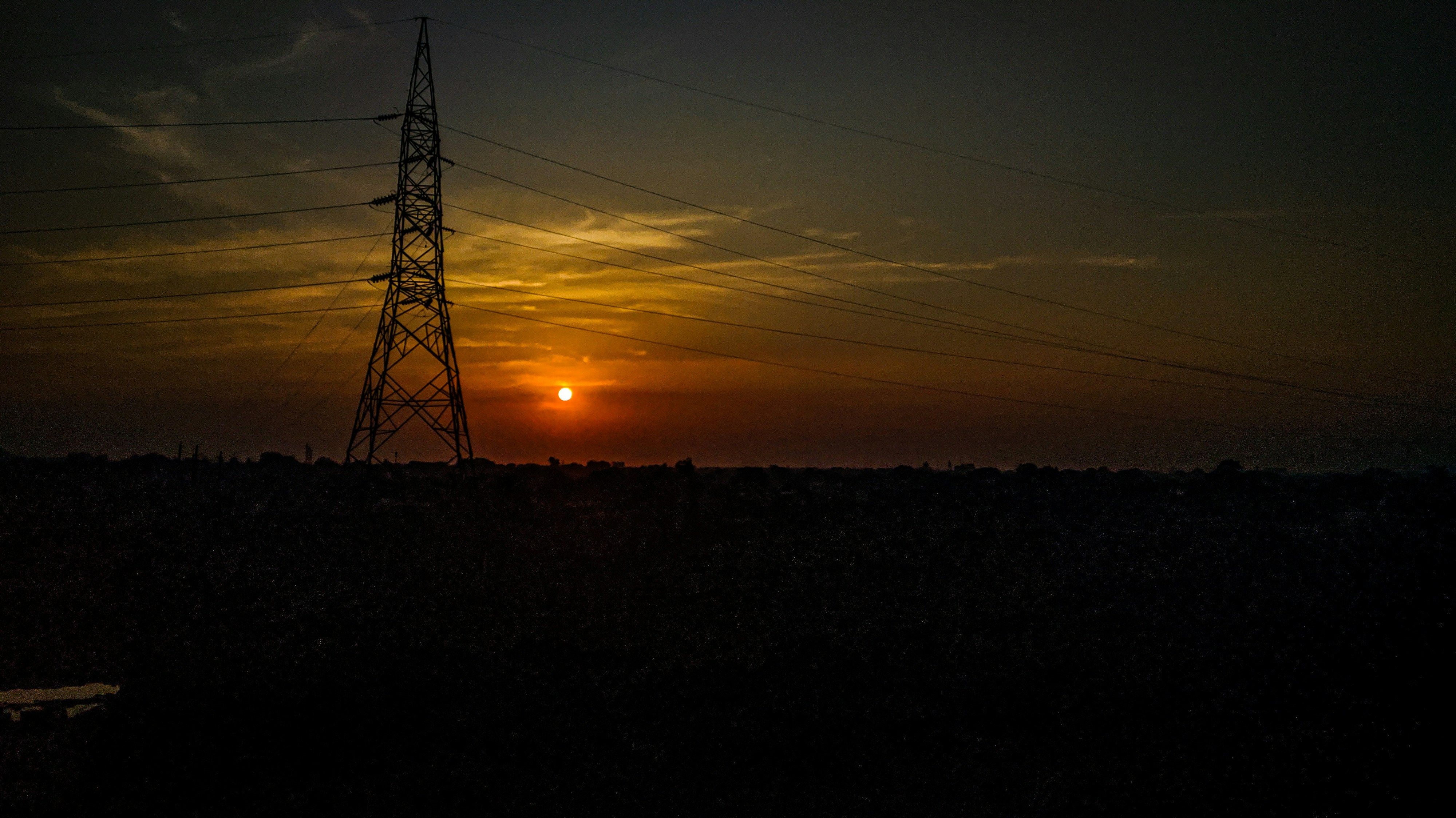 Silhouette of an electrical tower against a vibrant sunset sky with scattered clouds.