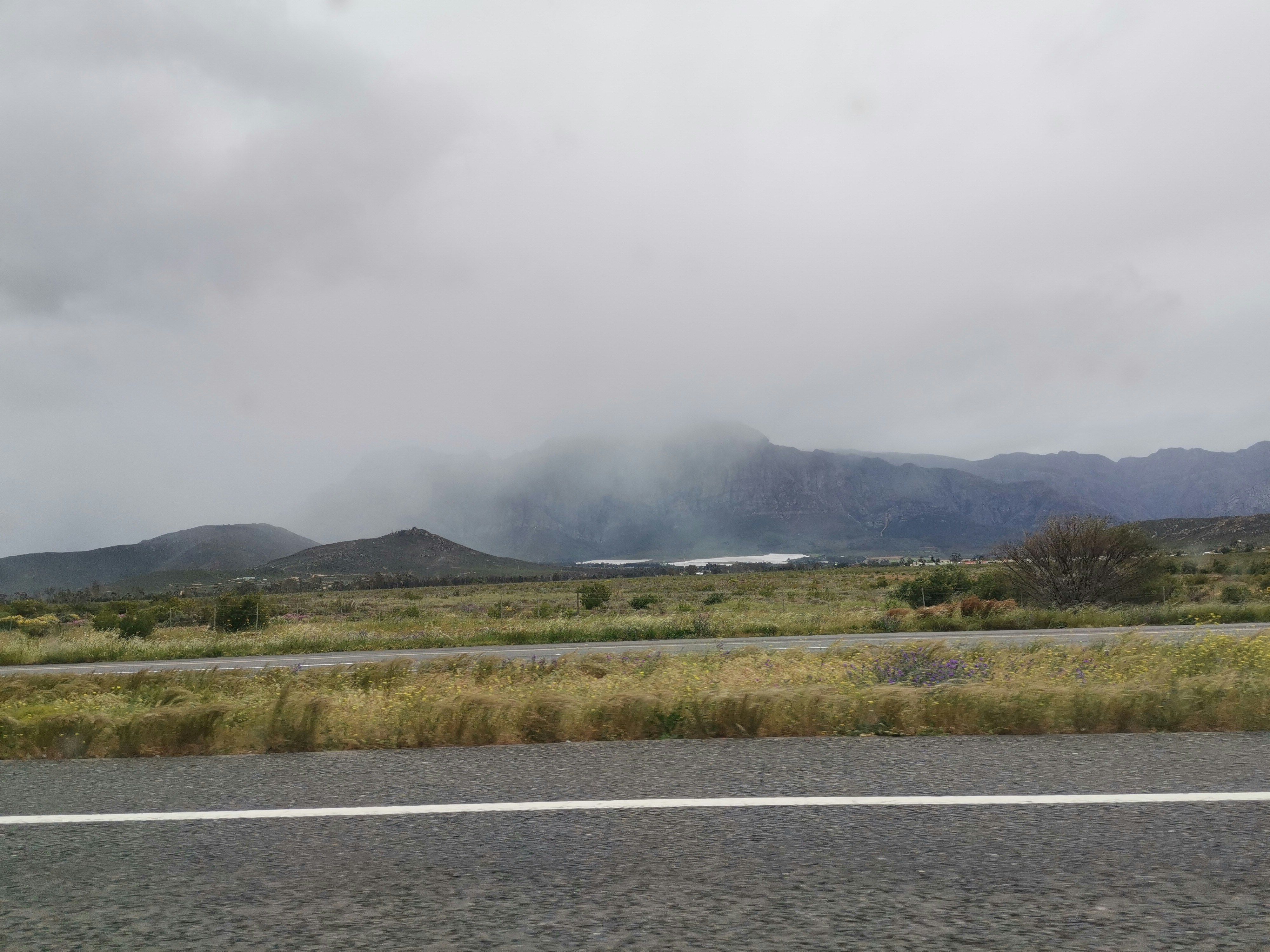 Clouds descend over distant mountains with grassy fields in the foreground under an overcast sky.