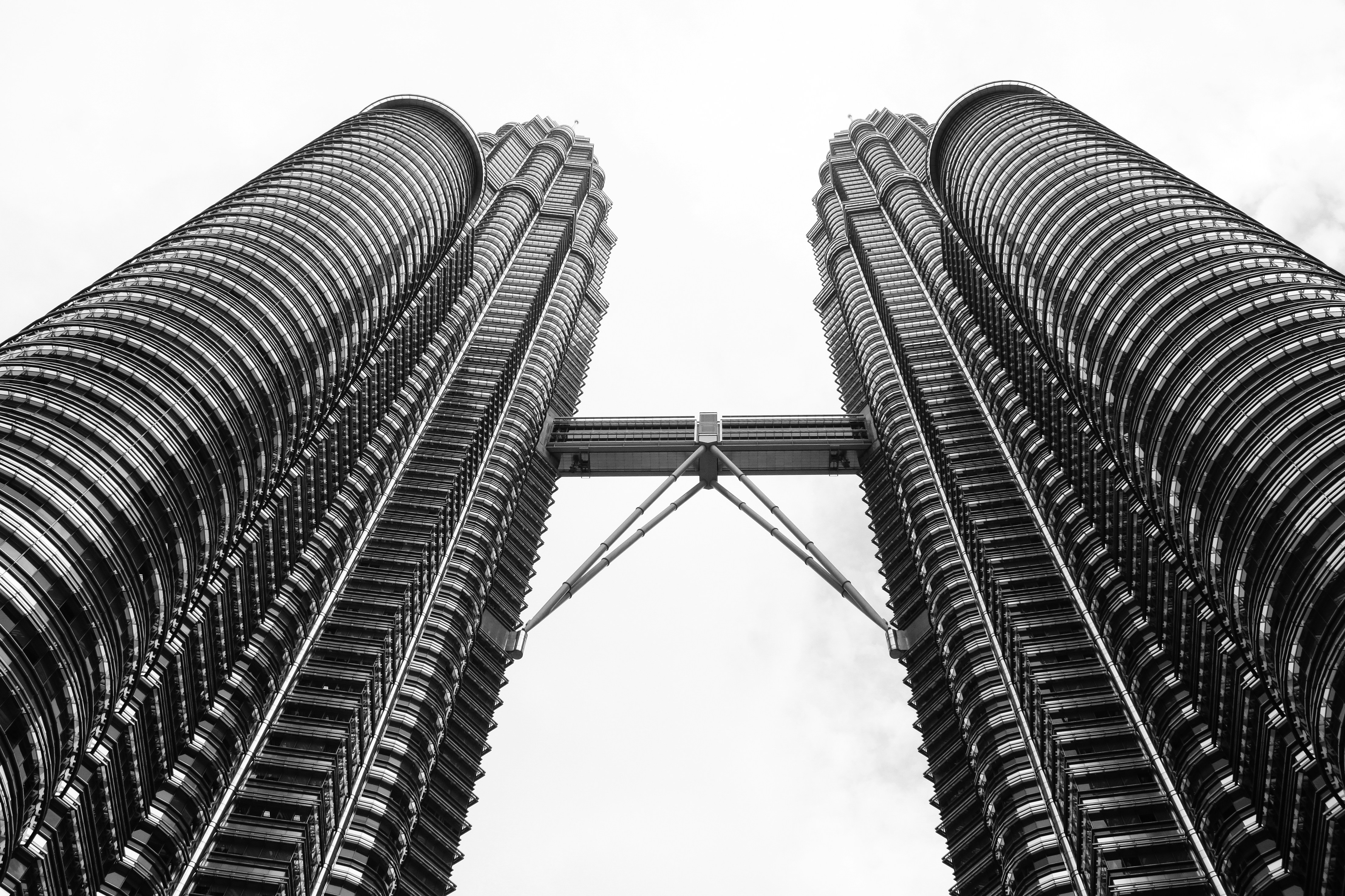 The Petronas Towers rise majestically against a cloudy sky, showcasing their intricate design and modern engineering. The image captures the towers' reflective surfaces and the bridge connecting them.