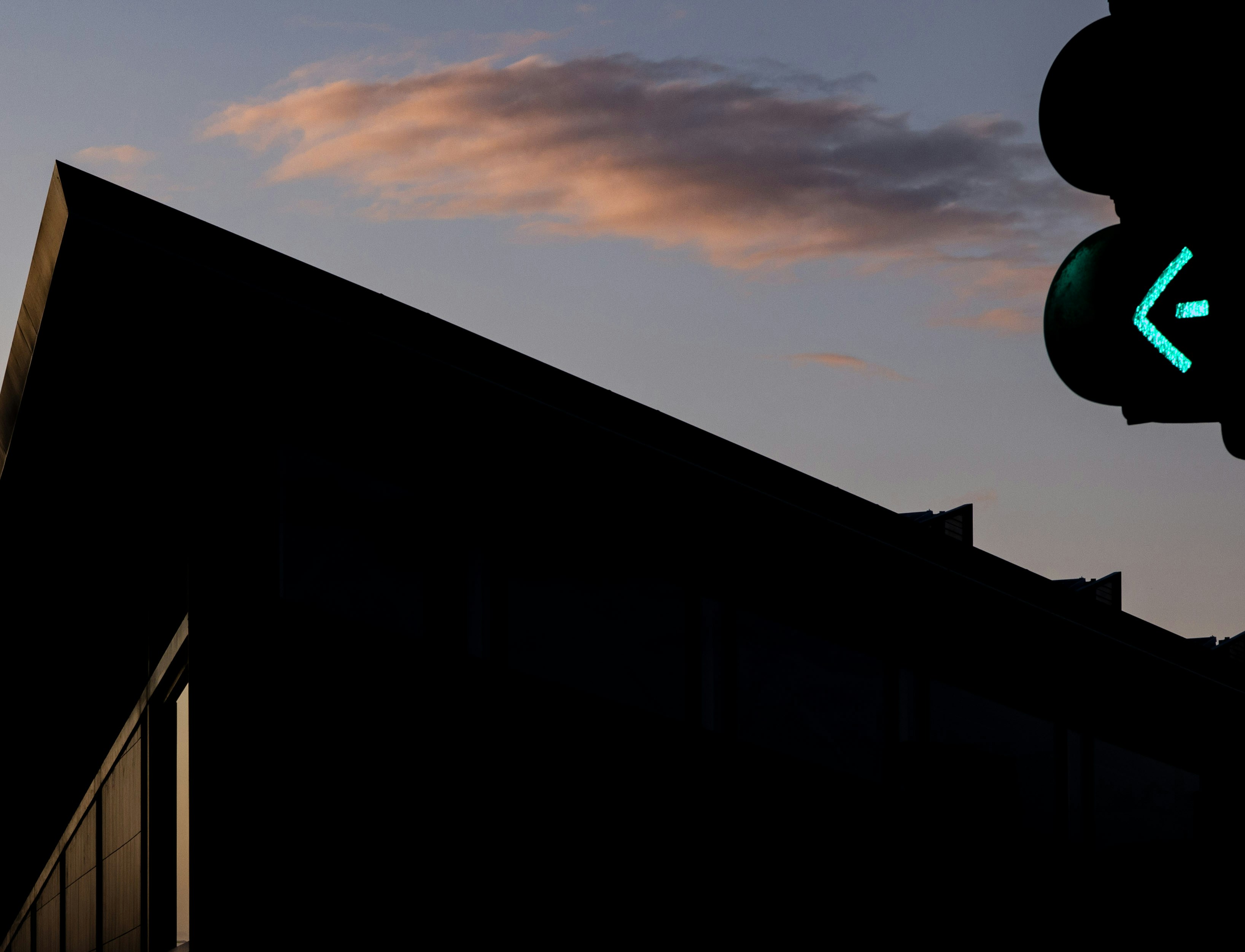 Silhouette of a building against a twilight sky, highlighted by a glowing green traffic signal. The contrast emphasizes urban life at dusk.