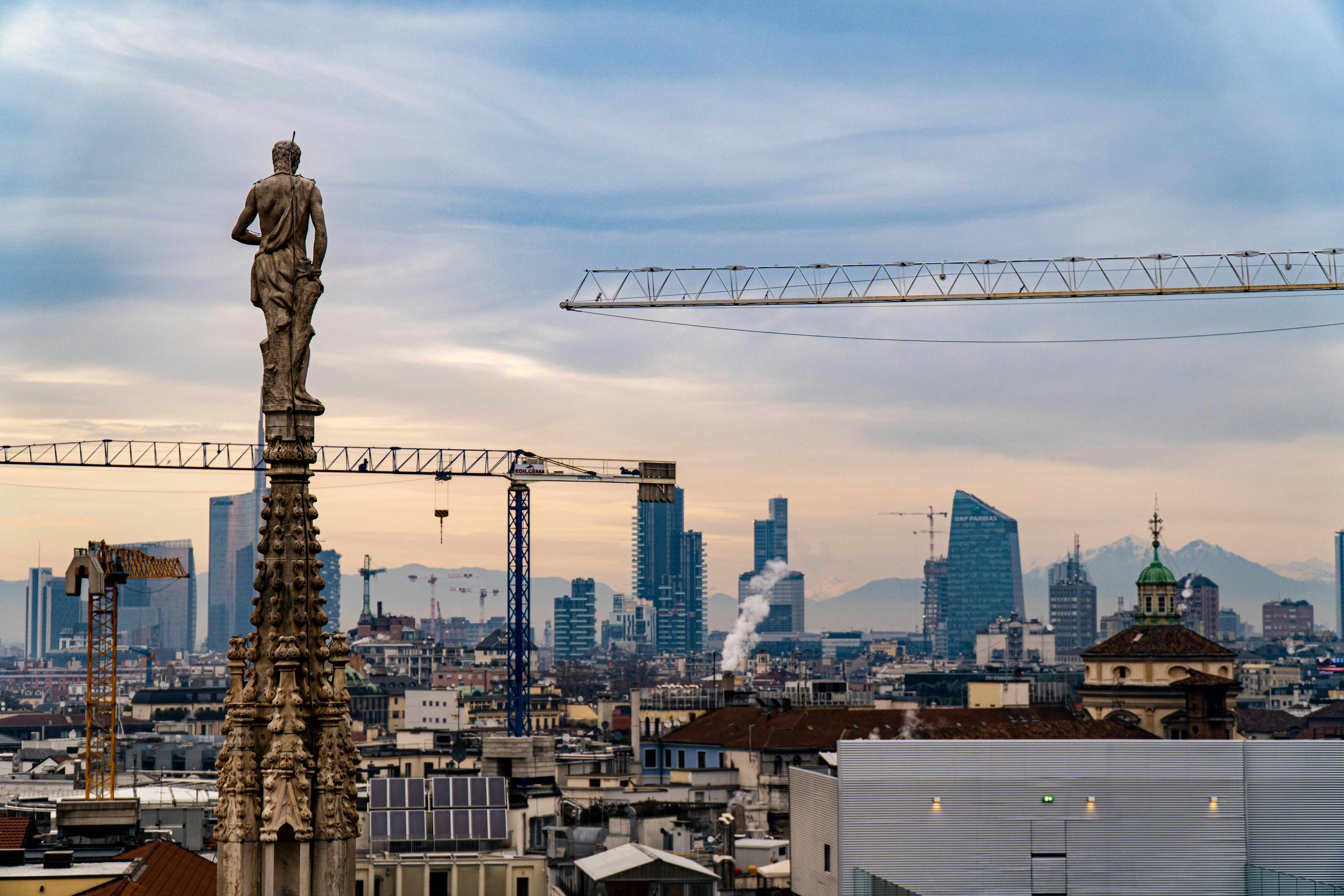 Stone Sentinel Over a Crane-filled Cityscape at Dusk