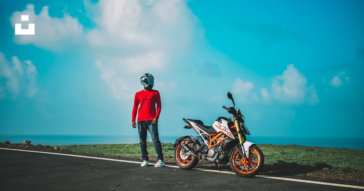 昼間、黒と白のバイクのそばに立つ赤いジャケットとブルーのデニムジーンズの男性の写真 Unsplashのディウの無料画像