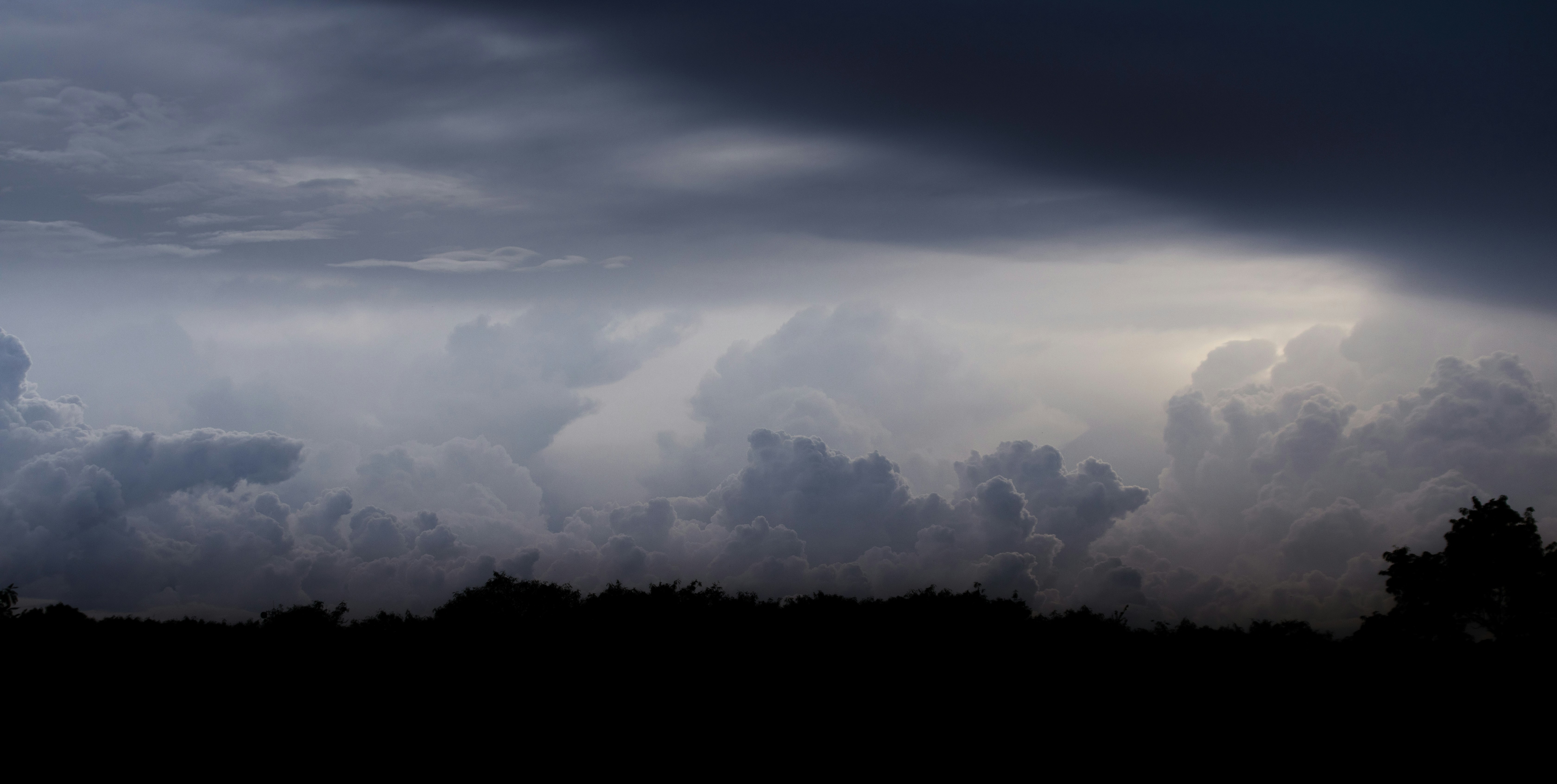 Dramatic dark clouds form above a silhouetted landscape as a storm approaches.