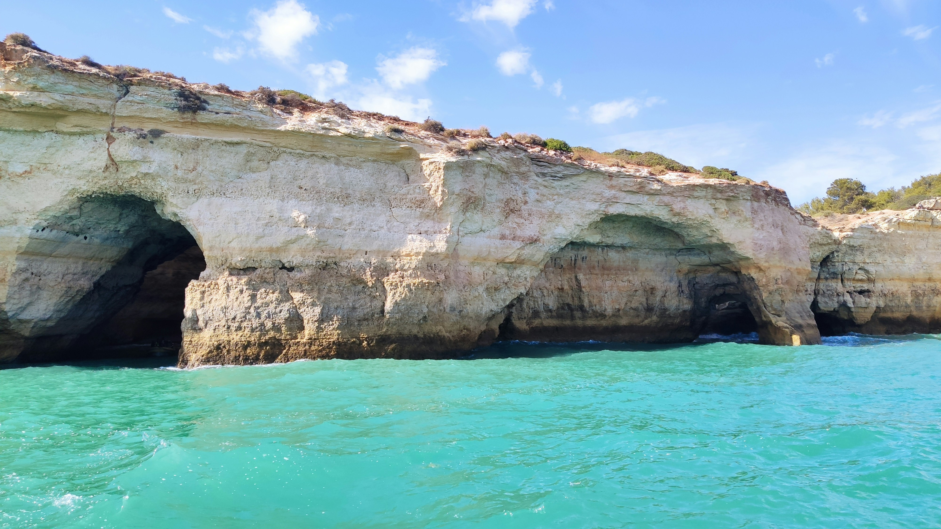 Turquoise waters lap against rugged coastal caves under a clear blue sky.