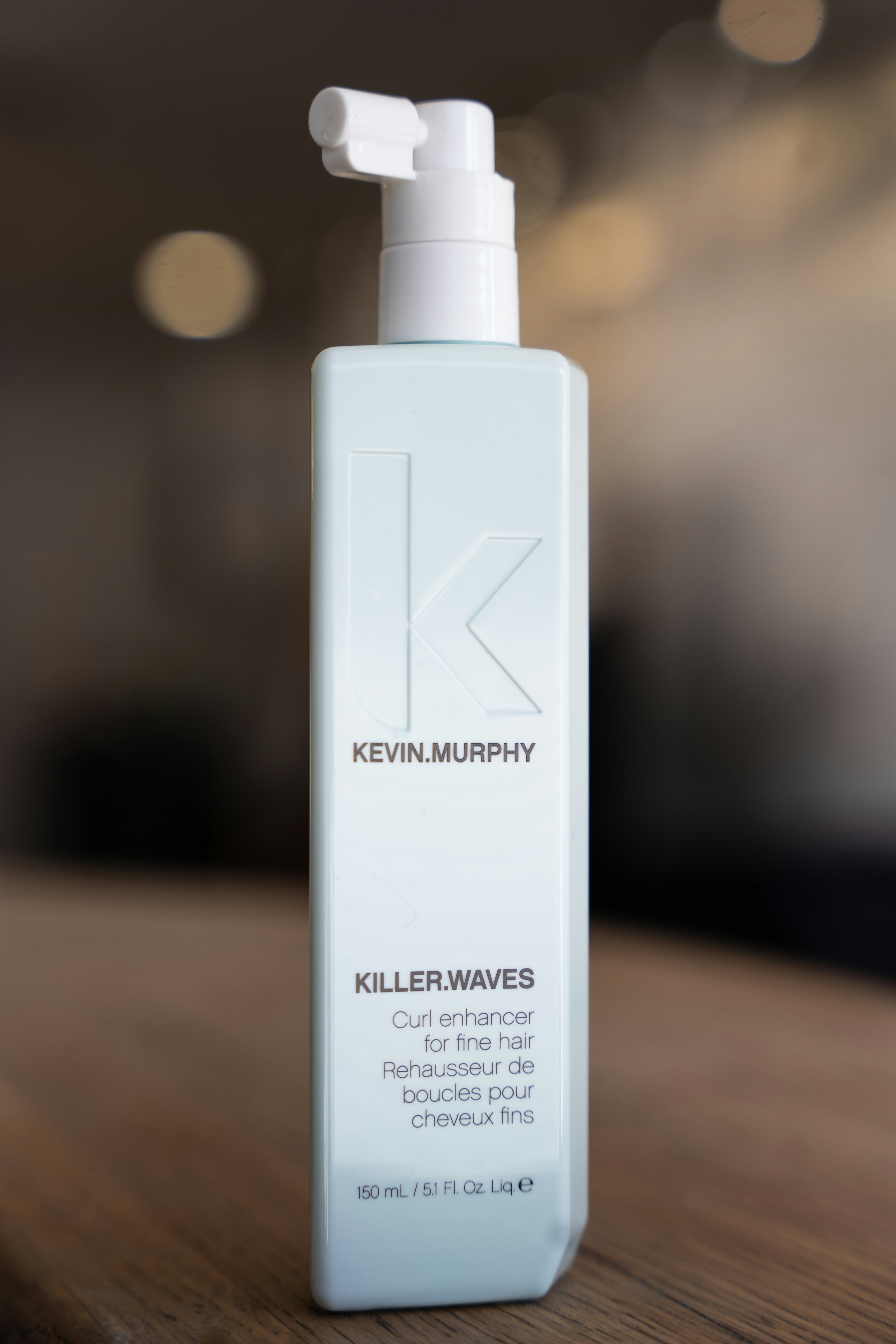 Bottle of KEVIN.MURPHY Killer.Waves curl enhancer for fine hair, displayed on a wooden surface with a blurred background.