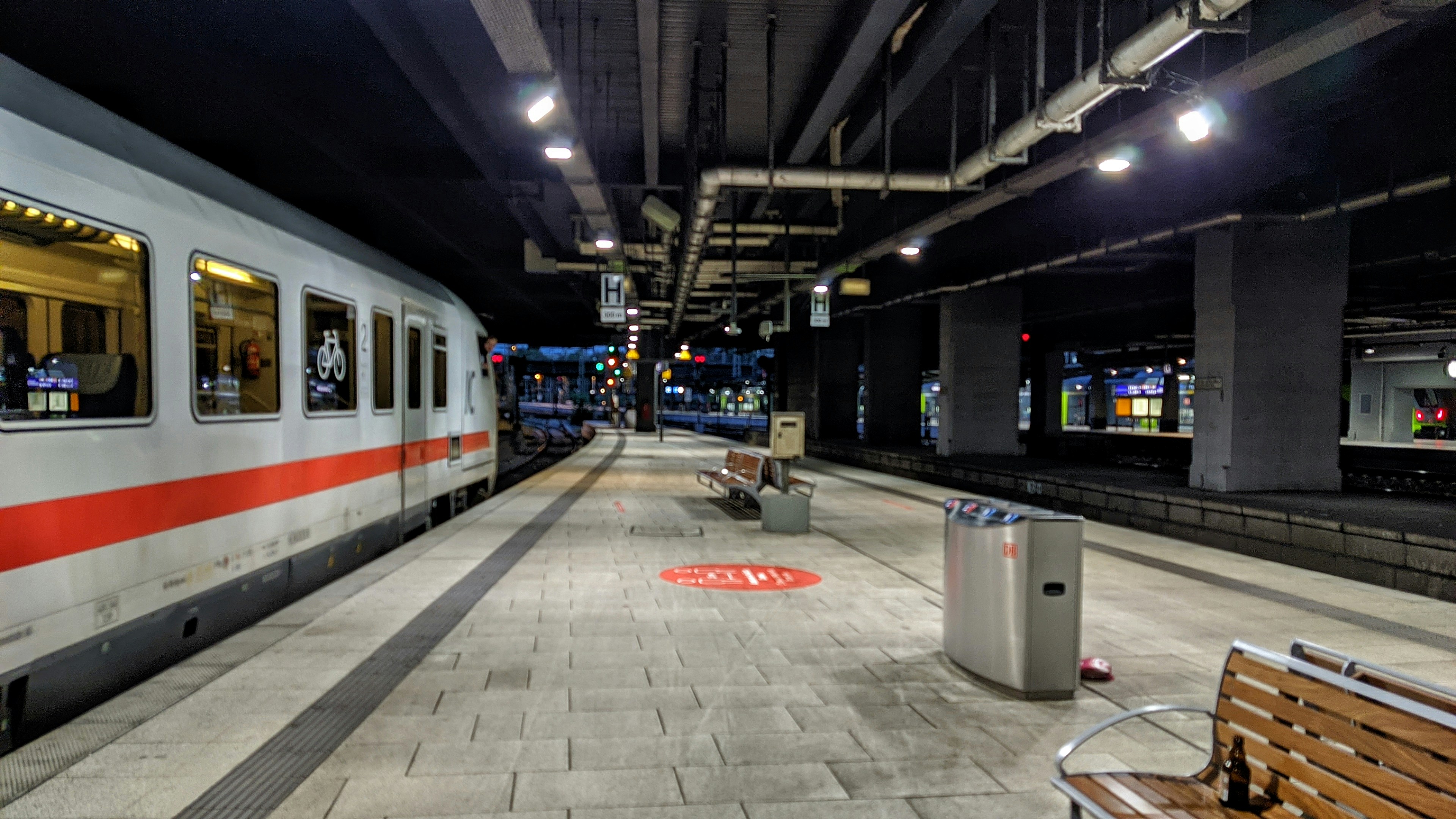 White and red train stationed on an empty platform under ambient lighting.