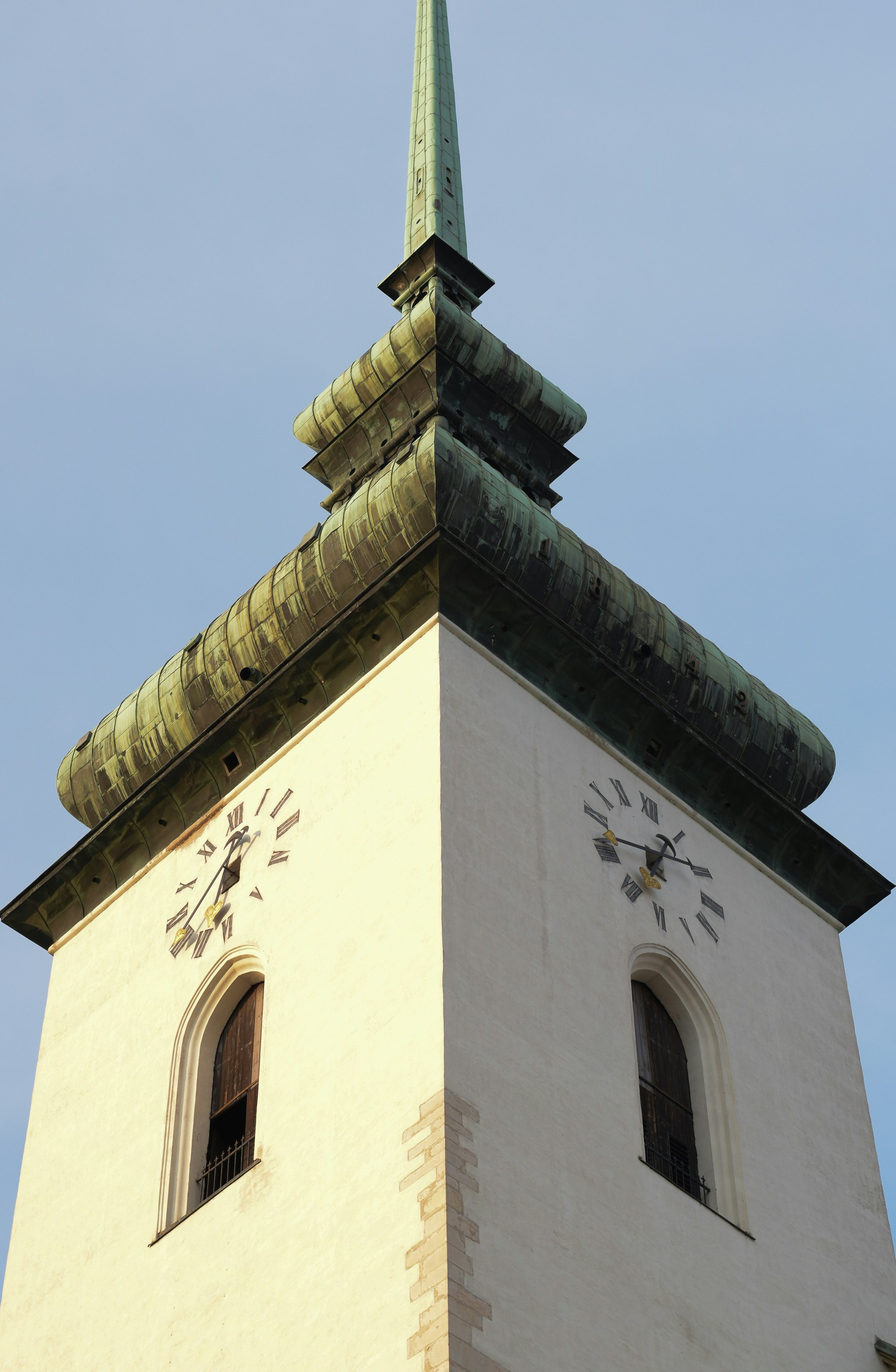 Historic clock tower with intricate details and a verdant spire reaching towards the sky.