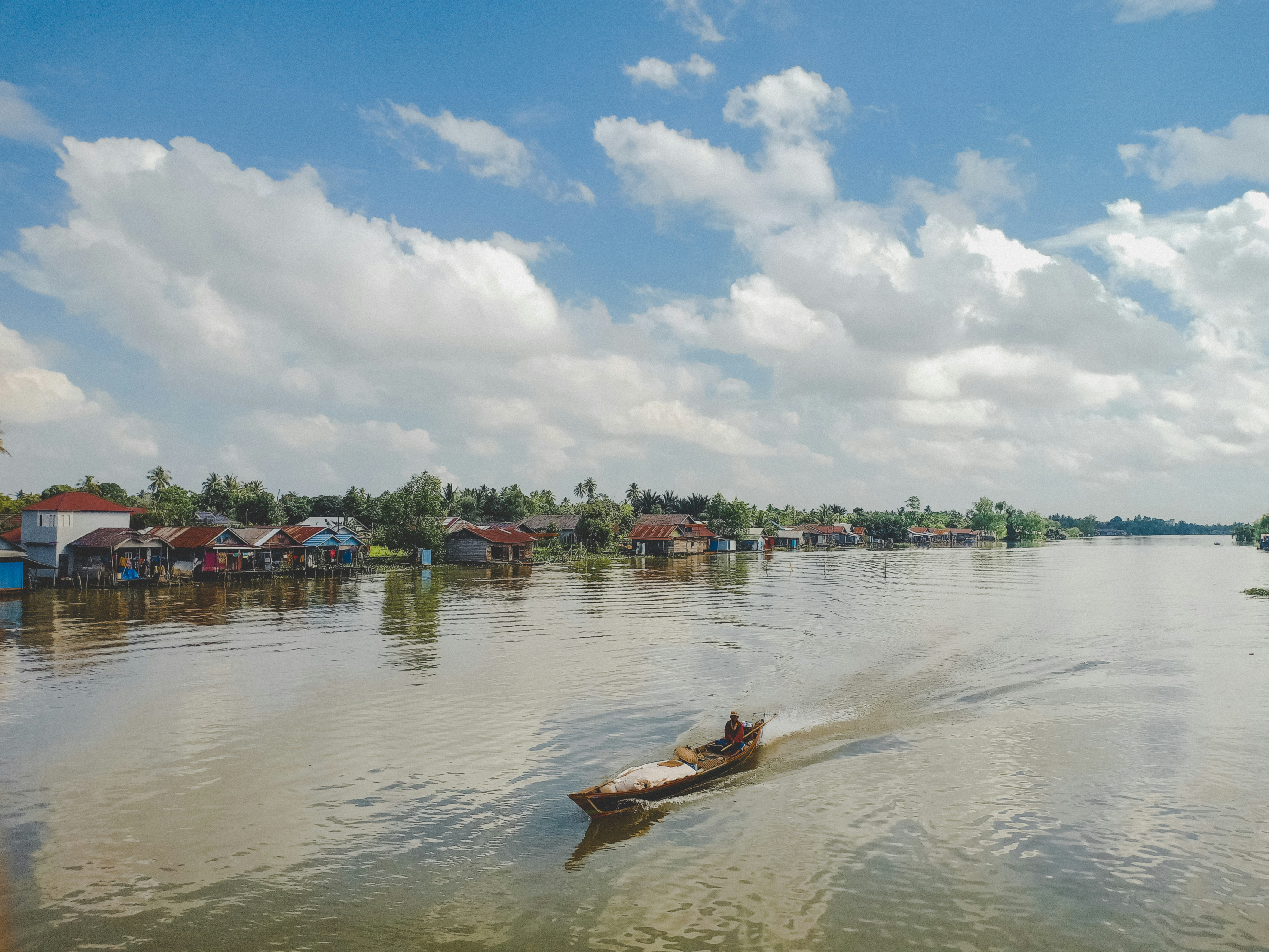 A boat glides through a tranquil river, surrounded by colorful houses perched on stilts, reflecting the unique lifestyle of floating villages. 