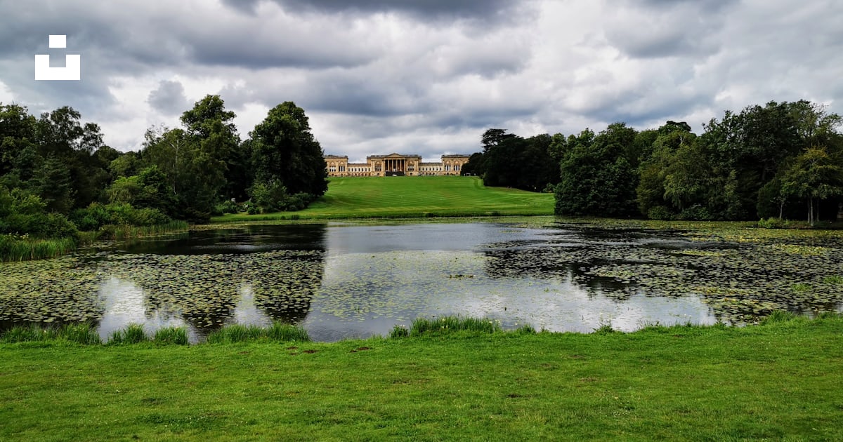 Green Grass Field Near River Under Cloudy Sky During Daytime Photo
