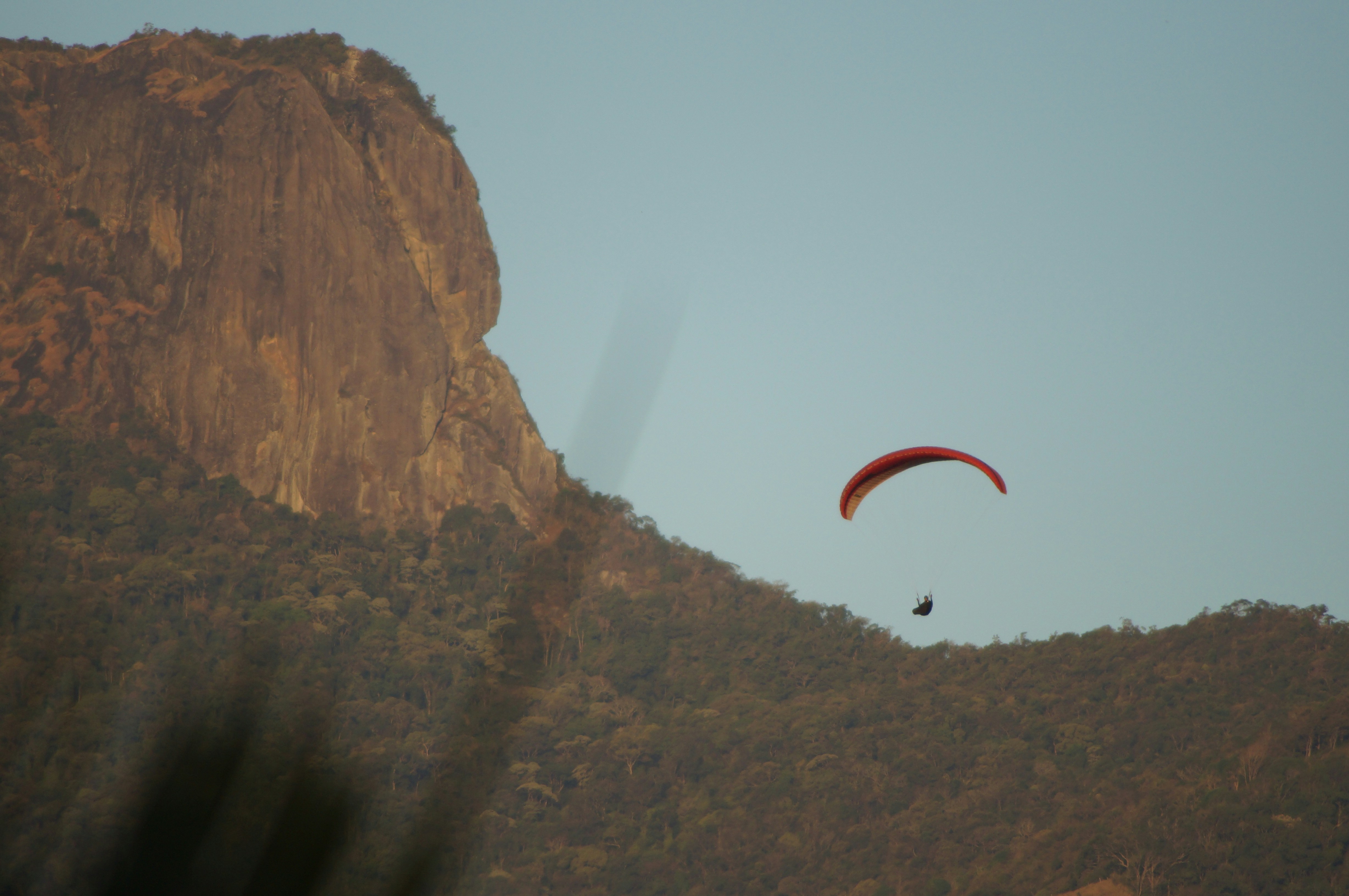 Crimson Paraglider Tracing a Mountain Ridge Under a Clear Blue Sky