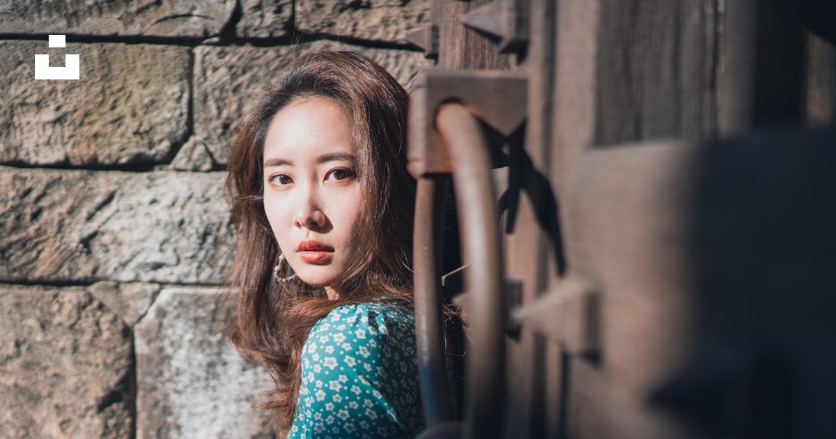 파란색과 검은색 긴팔 셔츠를 입은 여자가 갈색 벽돌 벽 옆에 서 있다 사진 Unsplash의 무료 의복 이미지