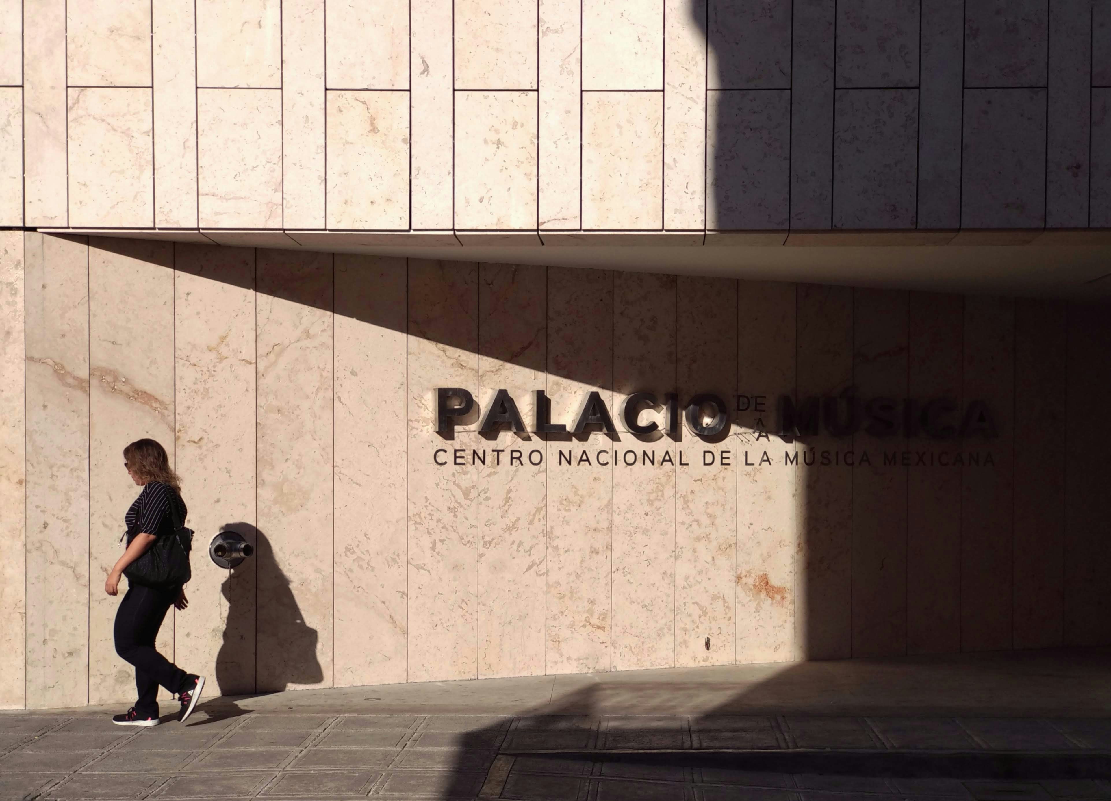A person strolls past the textured facade of the Palacio de Música, showcasing the architectural details of the Centro Nacional de la Música Mexicana.