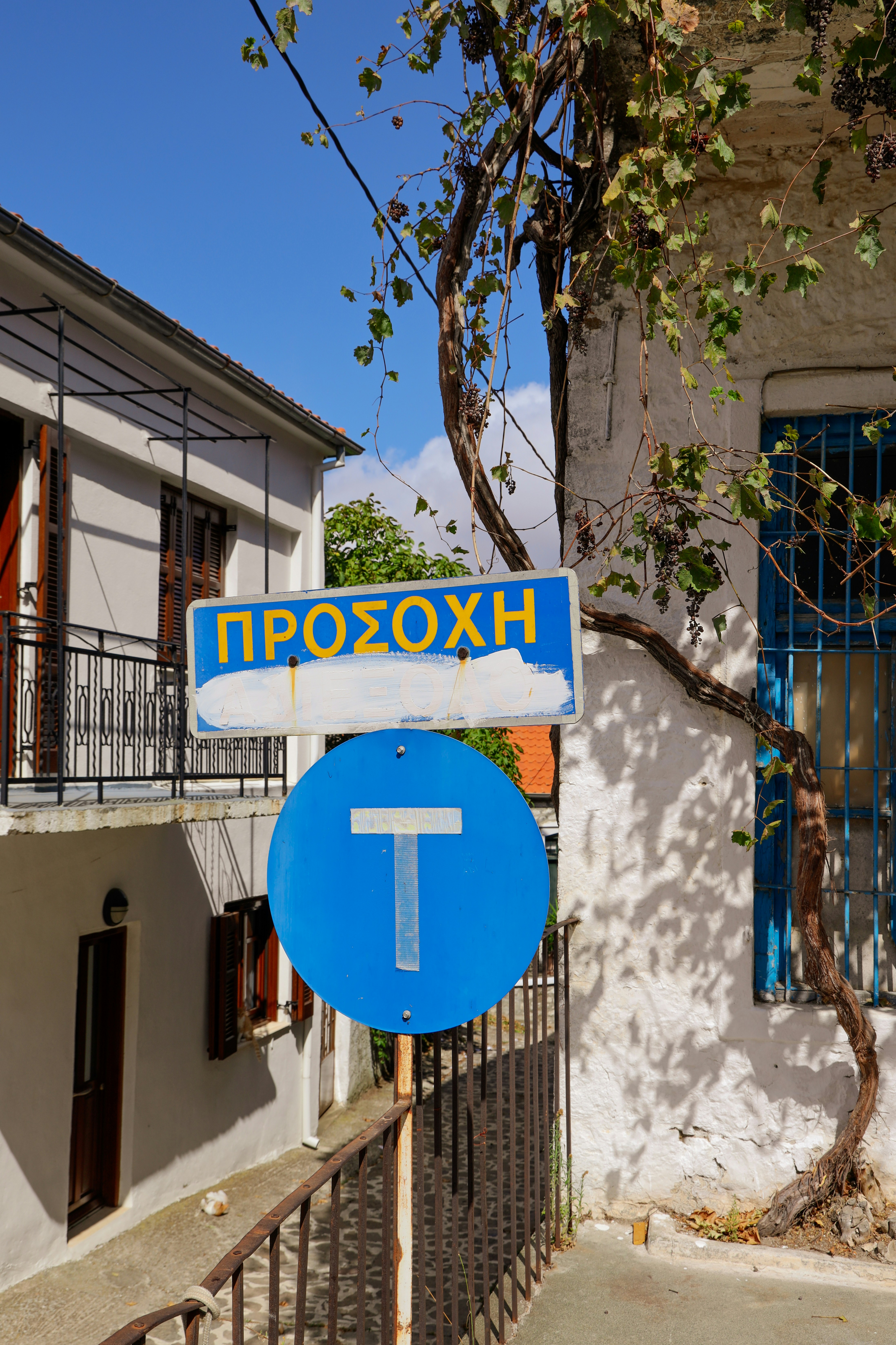 Caution in the Sun: A Blue Dead-End Sign Framed by Greek Villa Walls