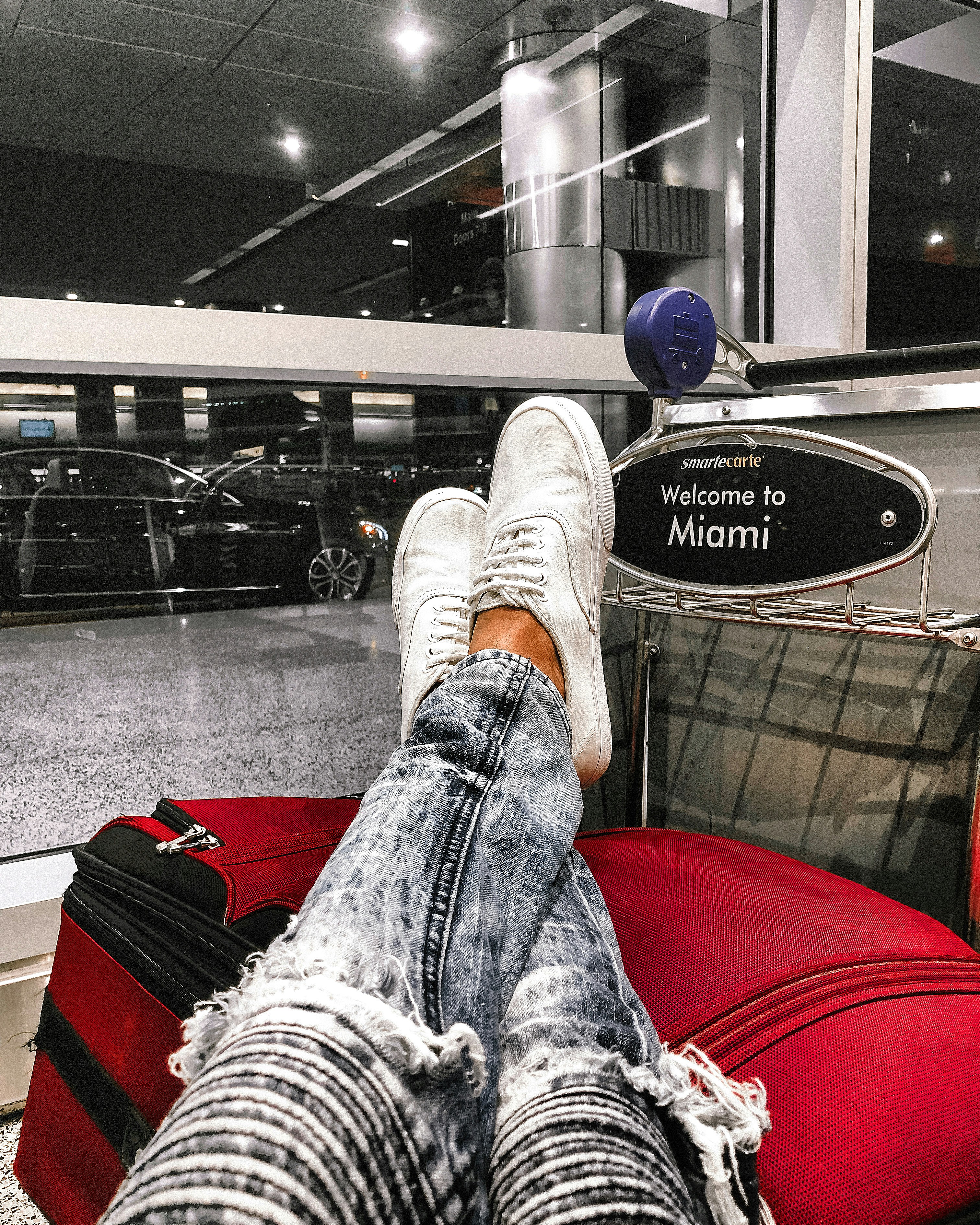 Mid-Stop Reverie: White Sneakers Rest Against a Miami Welcome Sign