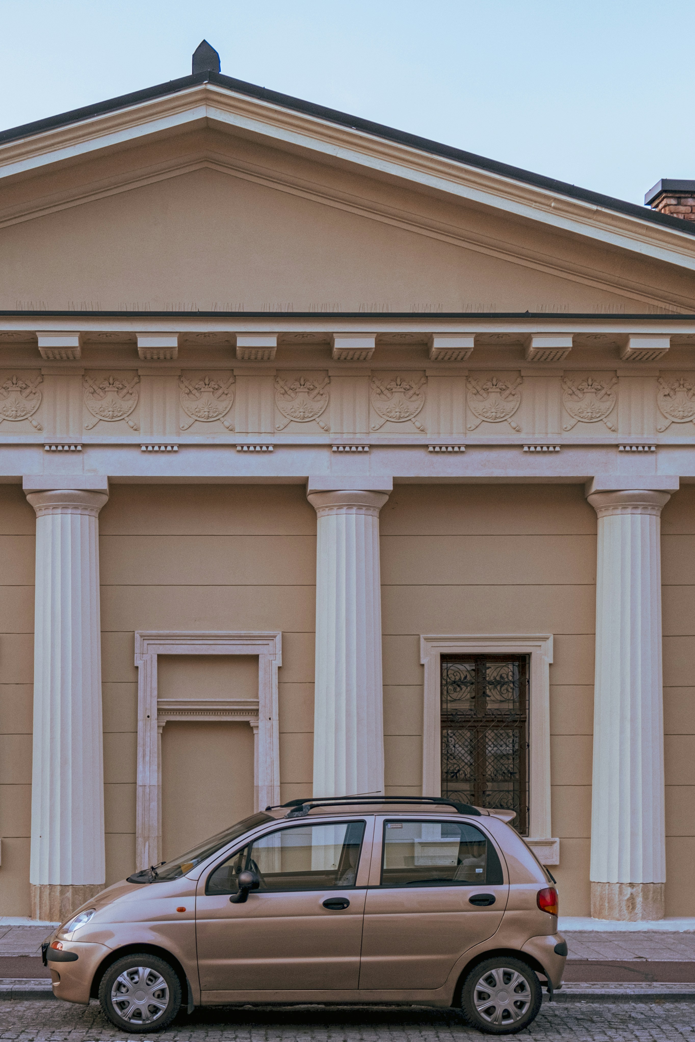Beige Microcar Beneath a Classical Portico: A Quiet Street Portrait