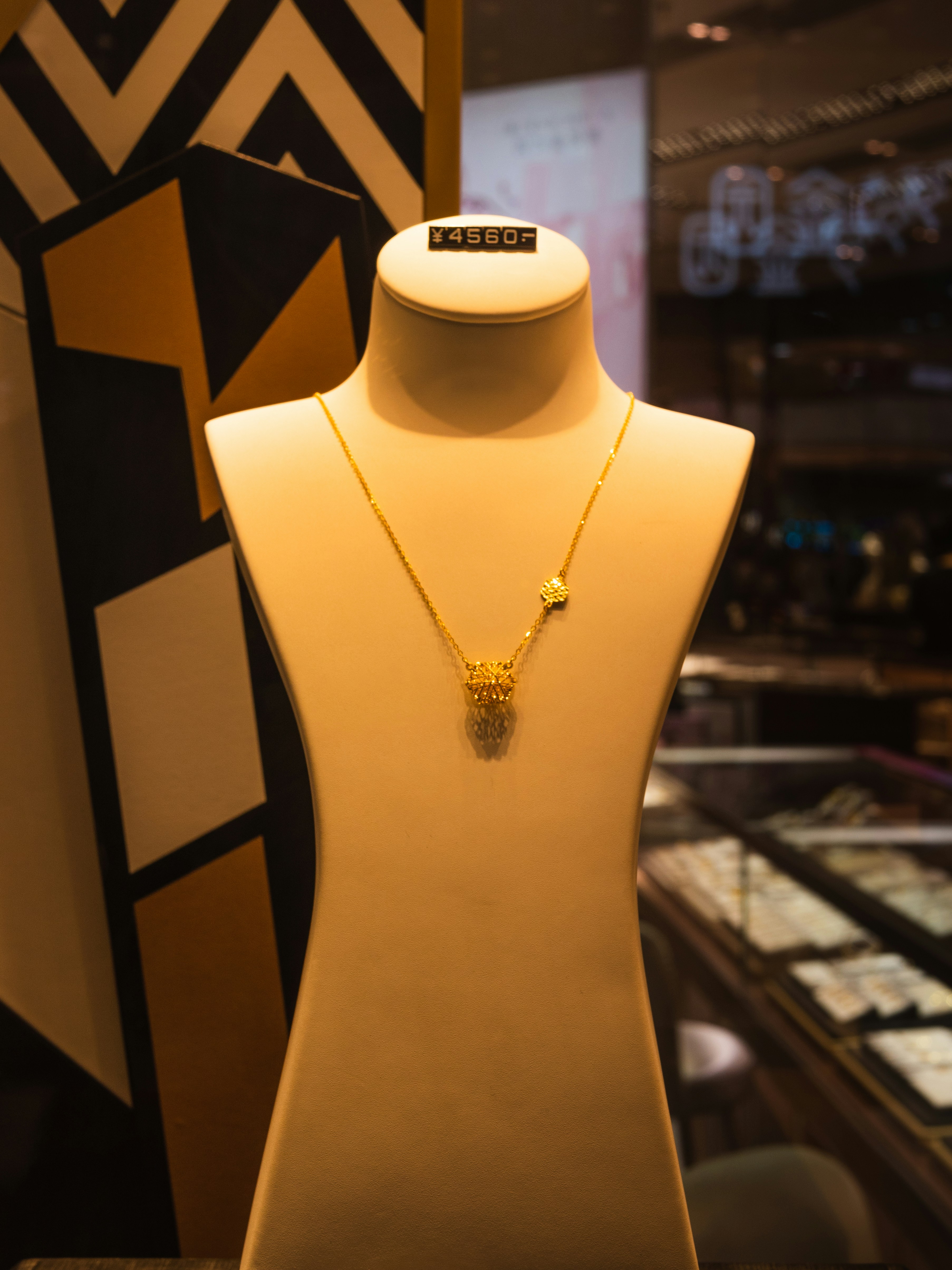 Amber Halo: Golden Necklace Glistens on a Minimalist Mannequin Display