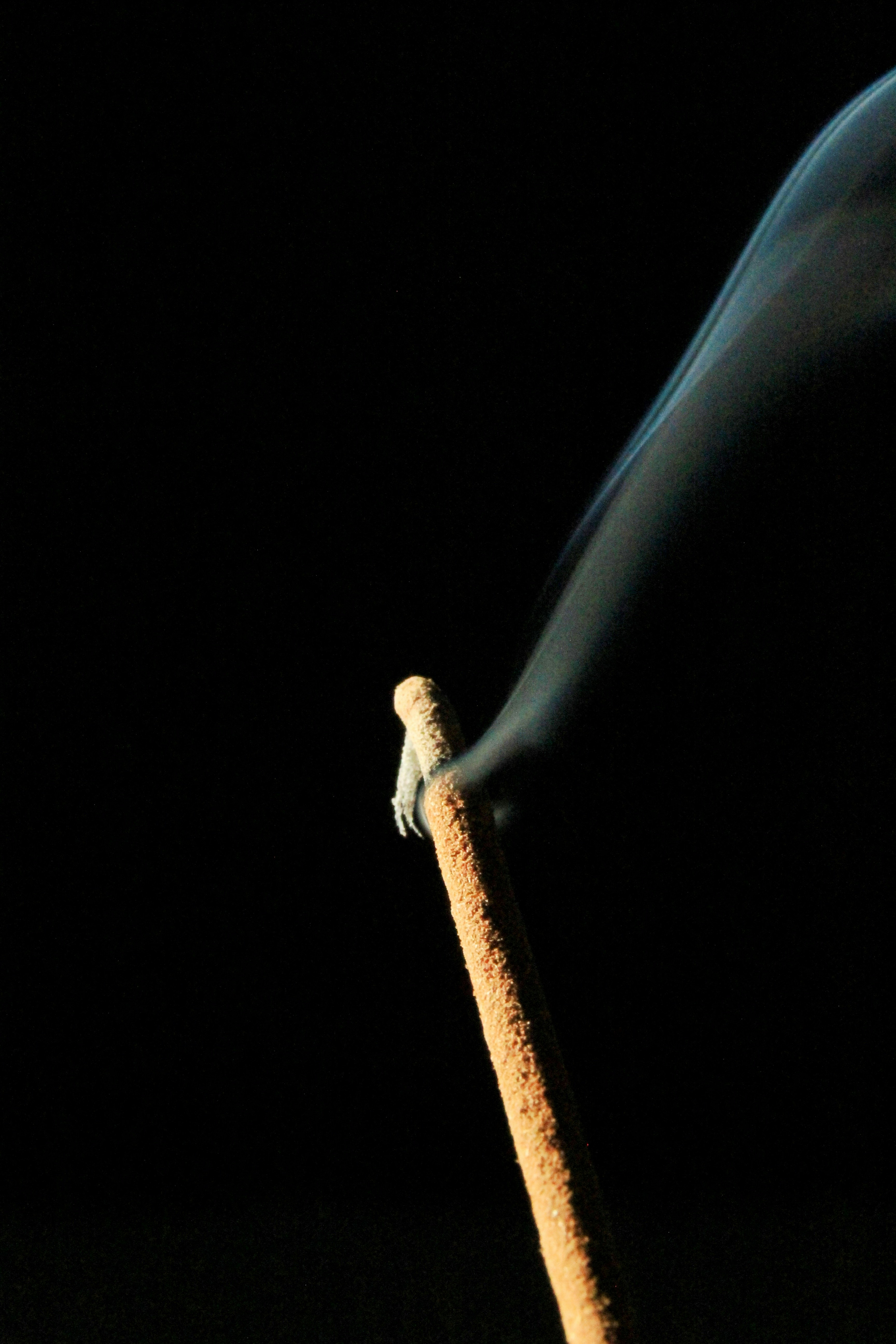Incense stick releasing a delicate plume of smoke against a dark backdrop, capturing the essence of tranquility.