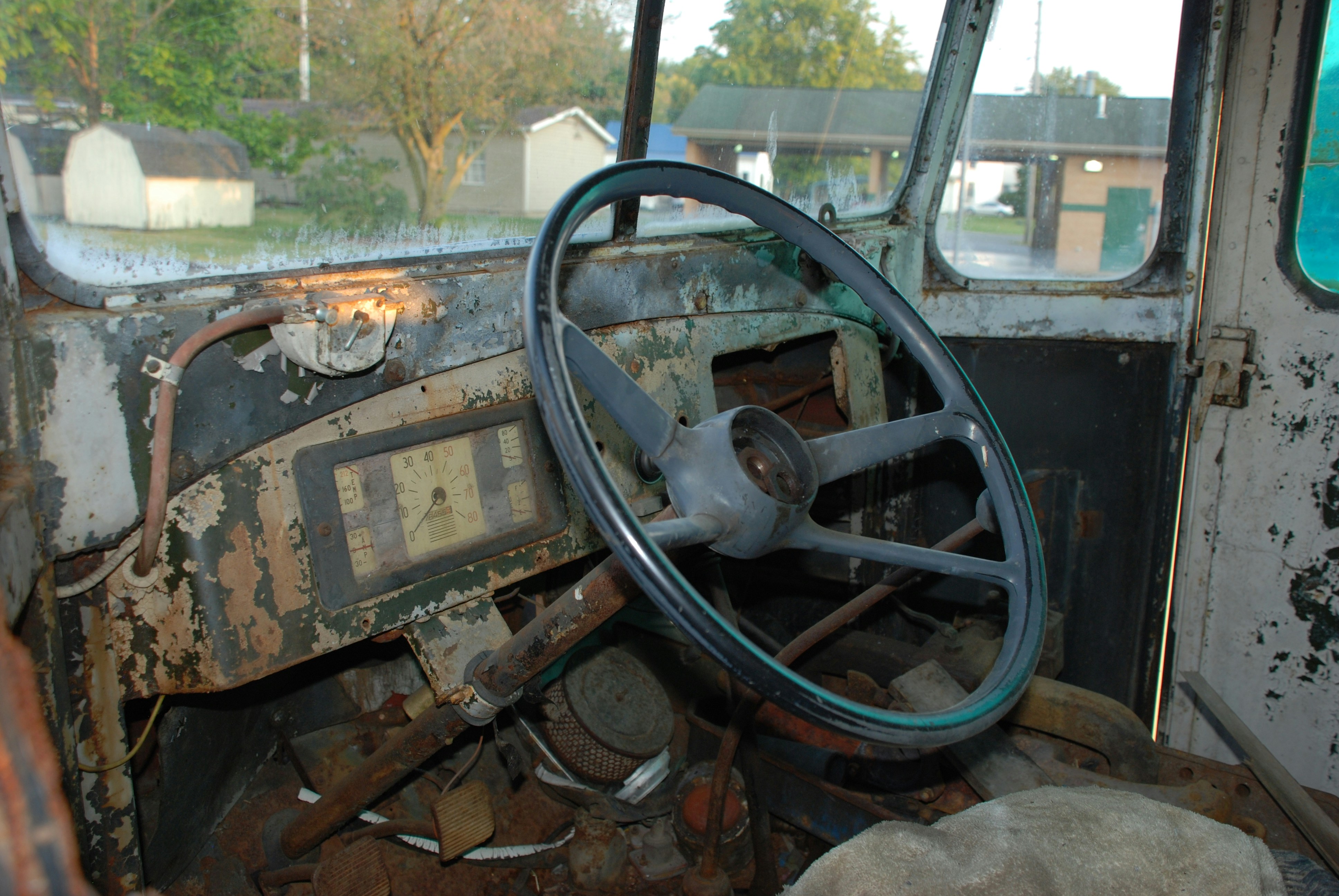 Rusty vintage truck interior showcasing a weathered steering wheel and dashboard, illustrating years of abandonment and history.