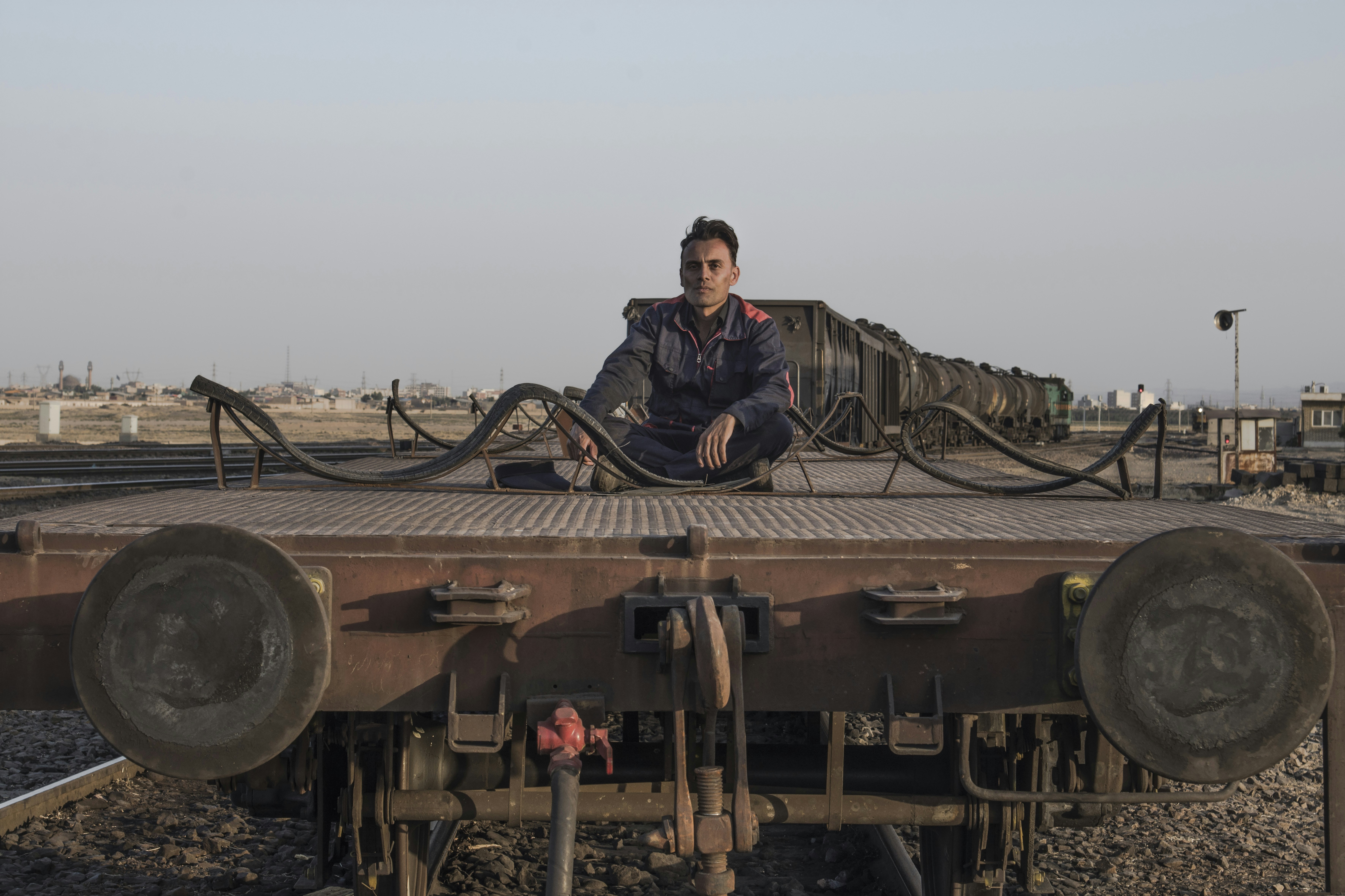 Man in black jacket sitting on brown metal train rail during daytime ...