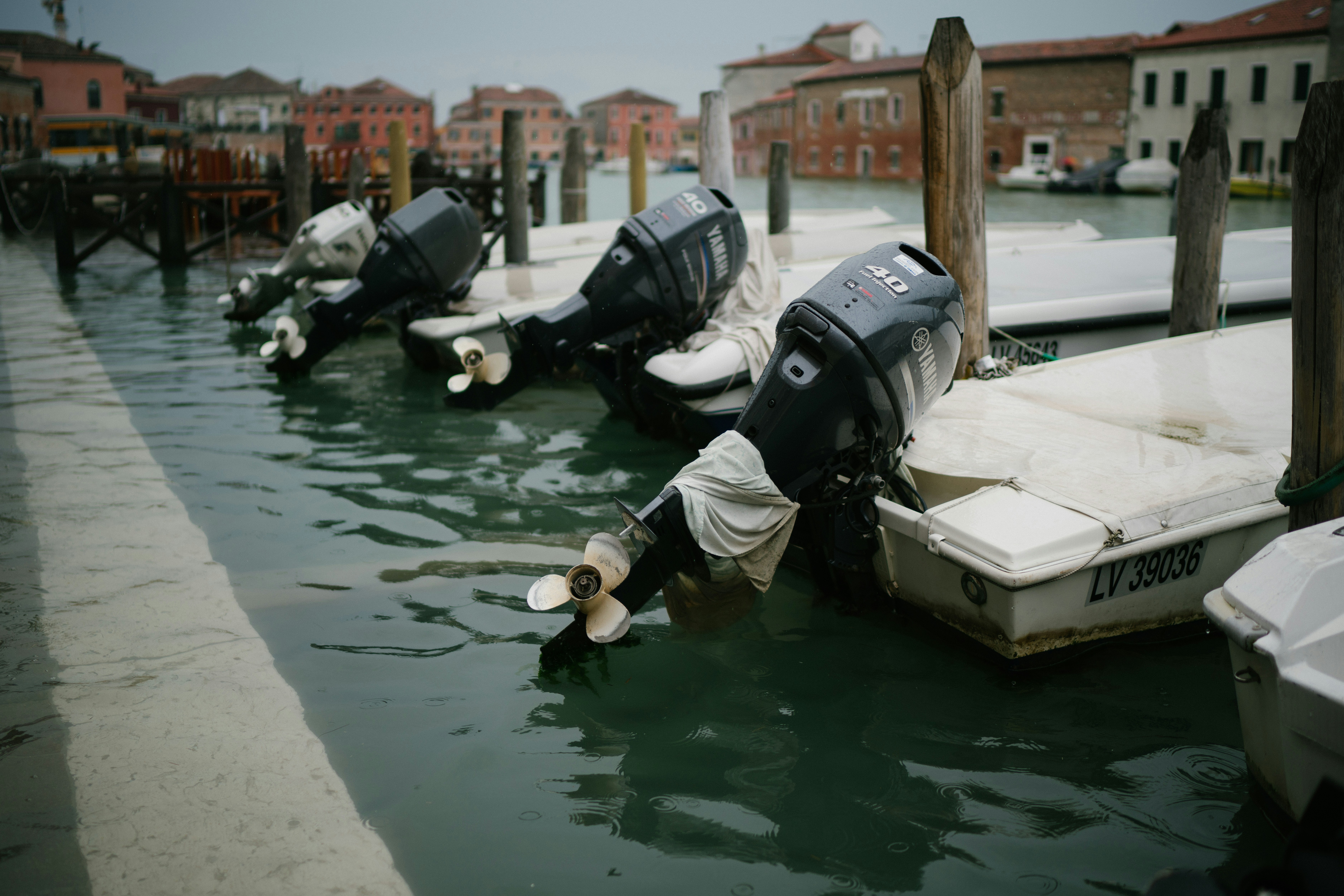 Outboard motors resting on boats in a tranquil marina, surrounded by historic buildings reflecting in the water. 