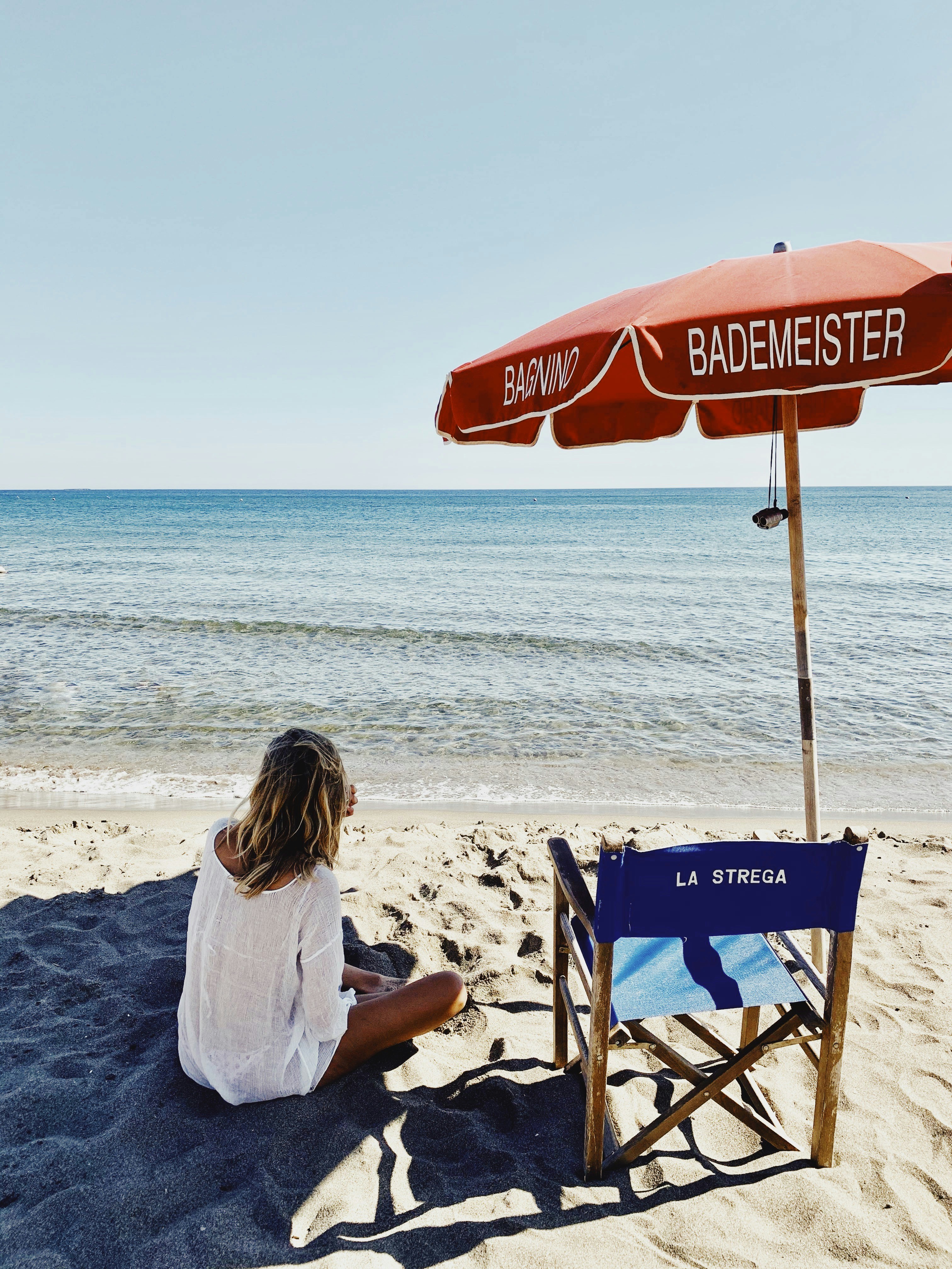 Mujer con camisa blanca sentada en silla azul y roja en la playa ...