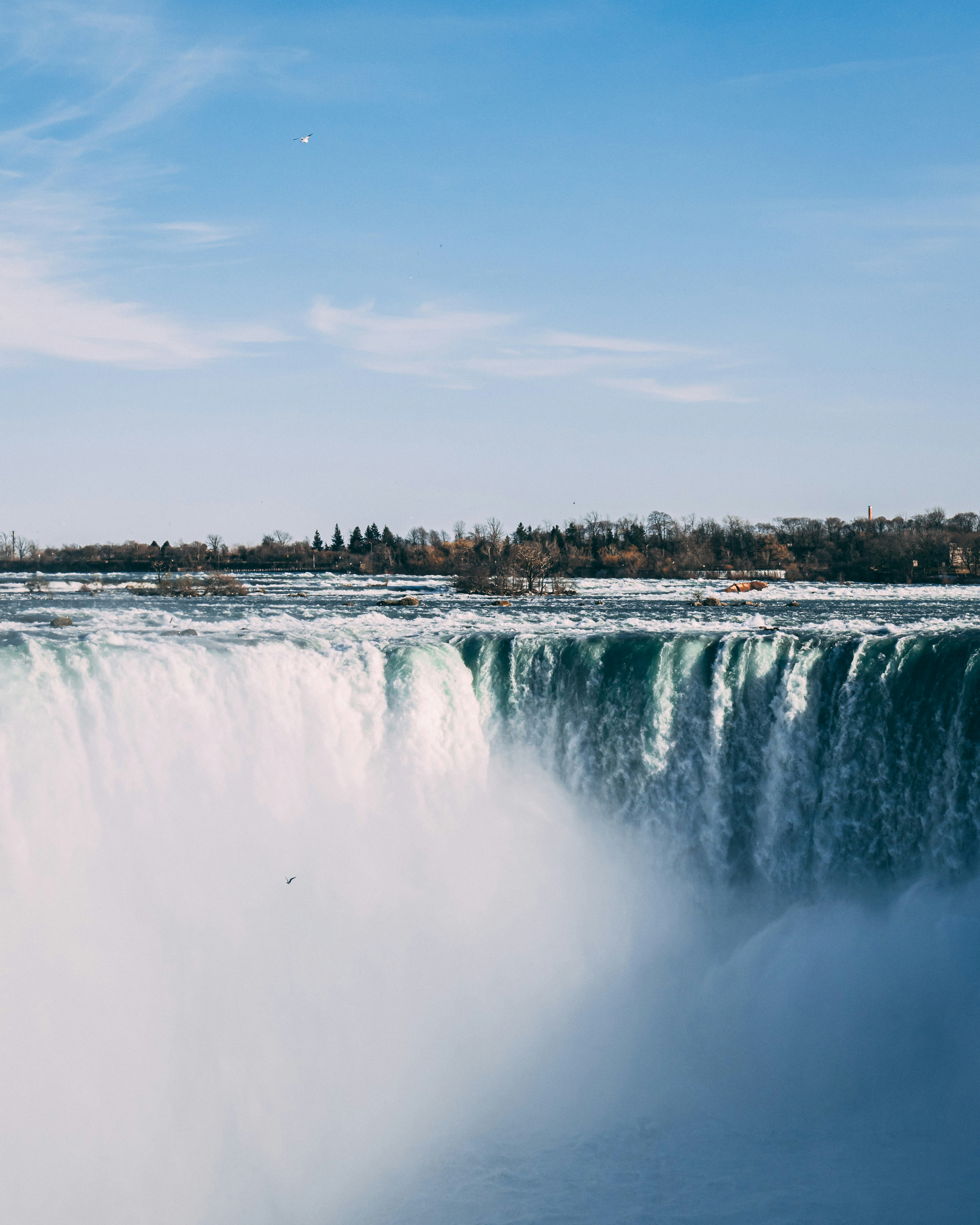 Cascading water plunges over a rocky precipice, enveloped in mist against a clear blue sky.
