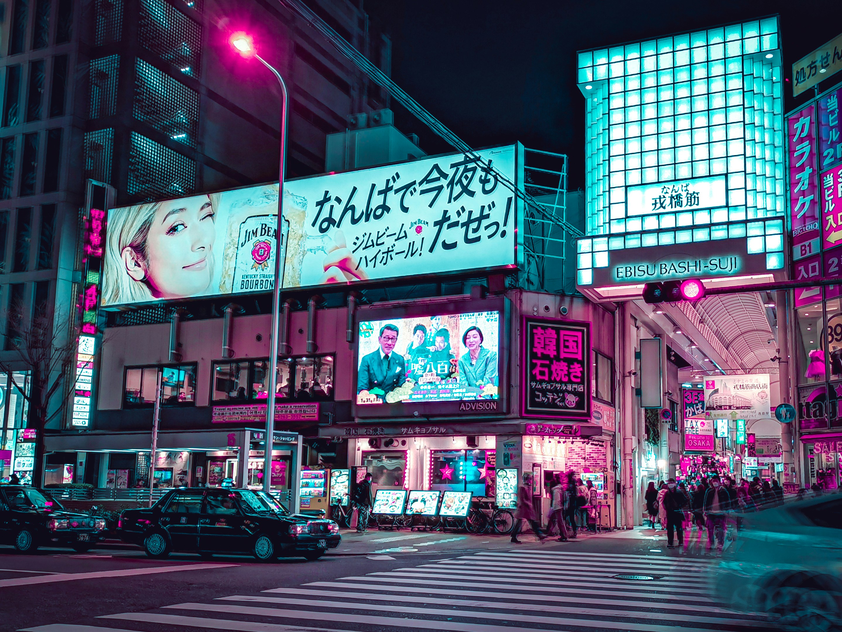 Night-time street scene dominated by neon billboards and pedestrians on a busy Japanese avenue.