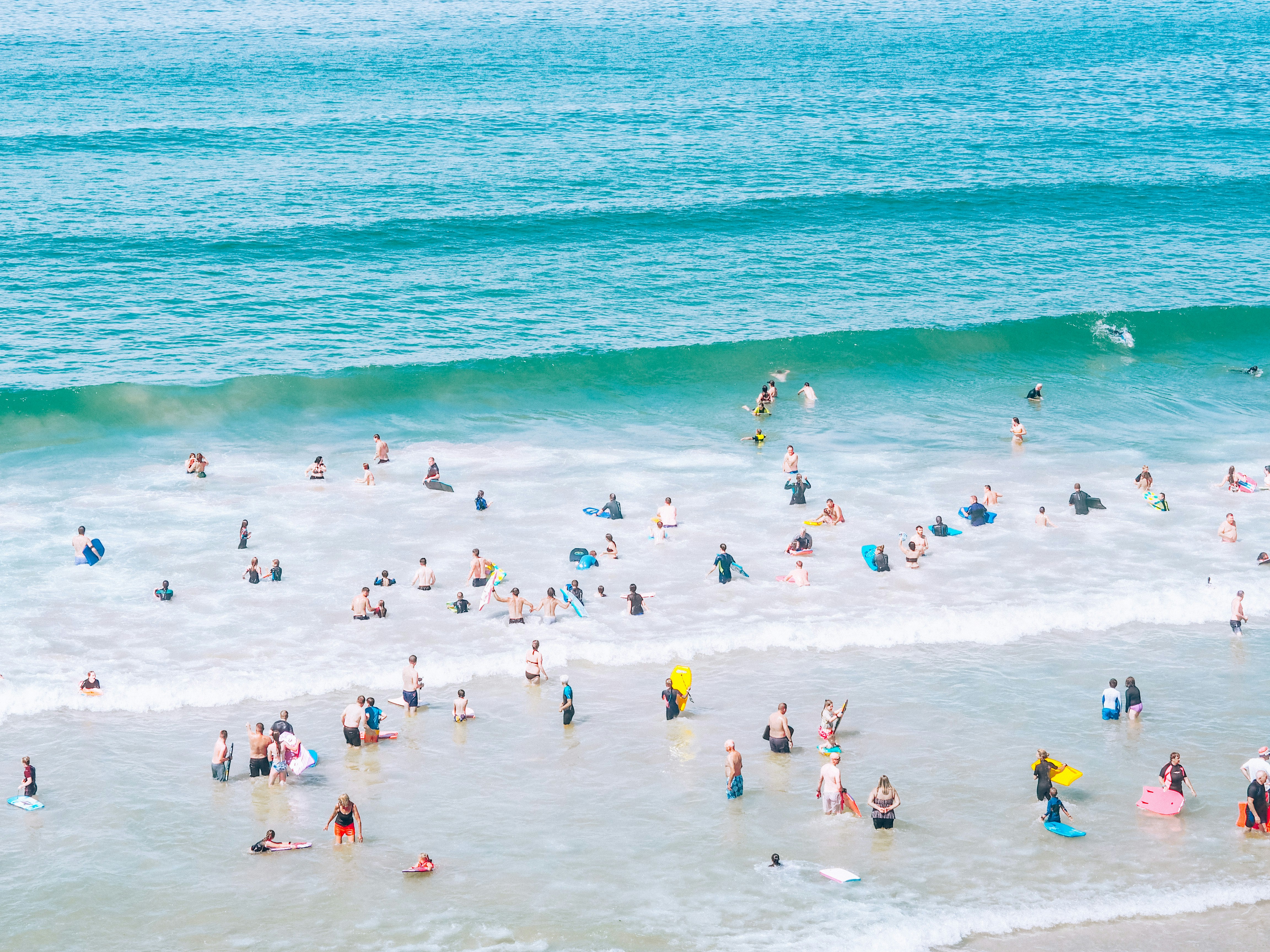 Crowded beach scene with people enjoying the waves and sandy shore under clear blue skies.