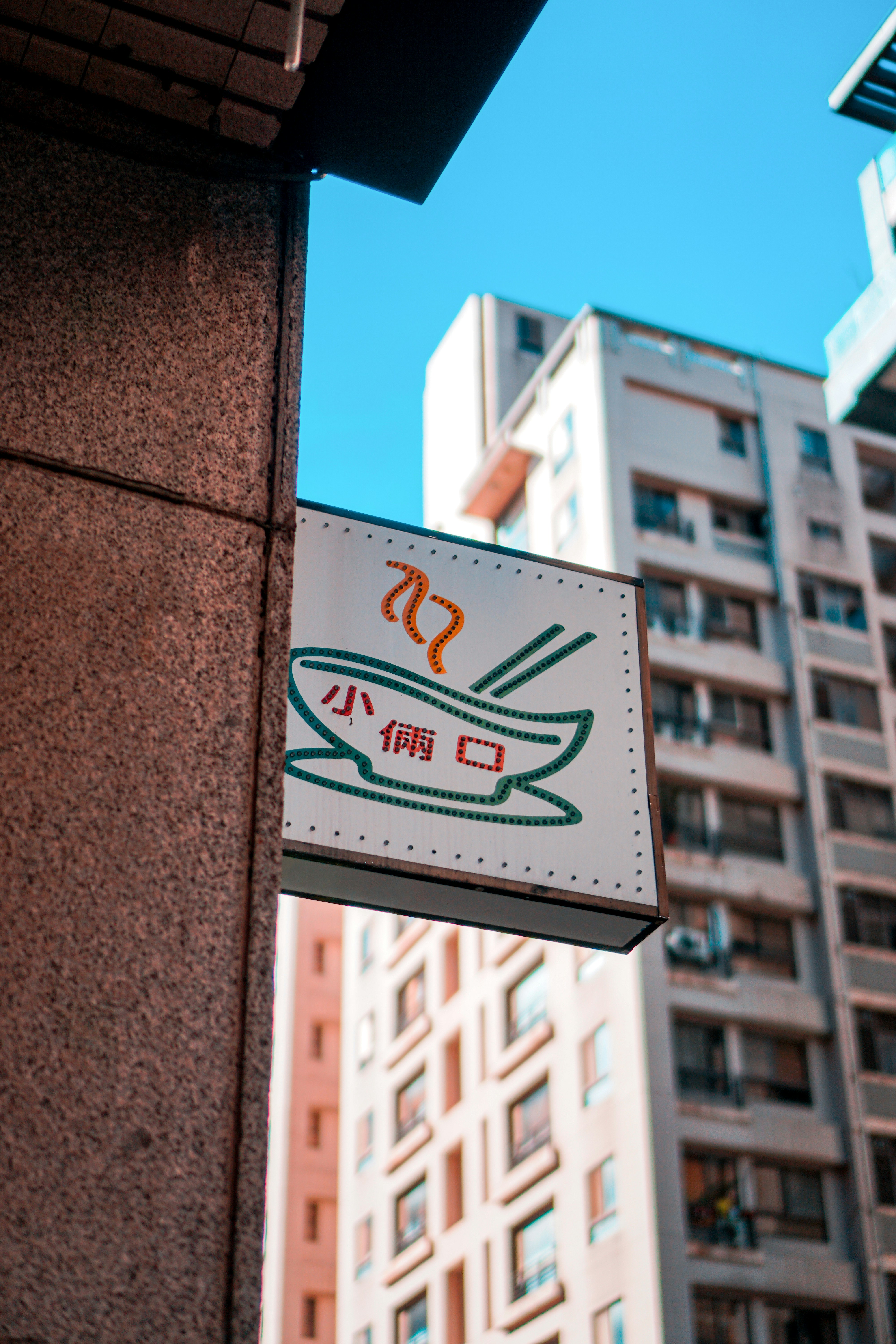 Colorful restaurant sign depicting a bowl of noodles with steam and chopsticks against an urban backdrop.
