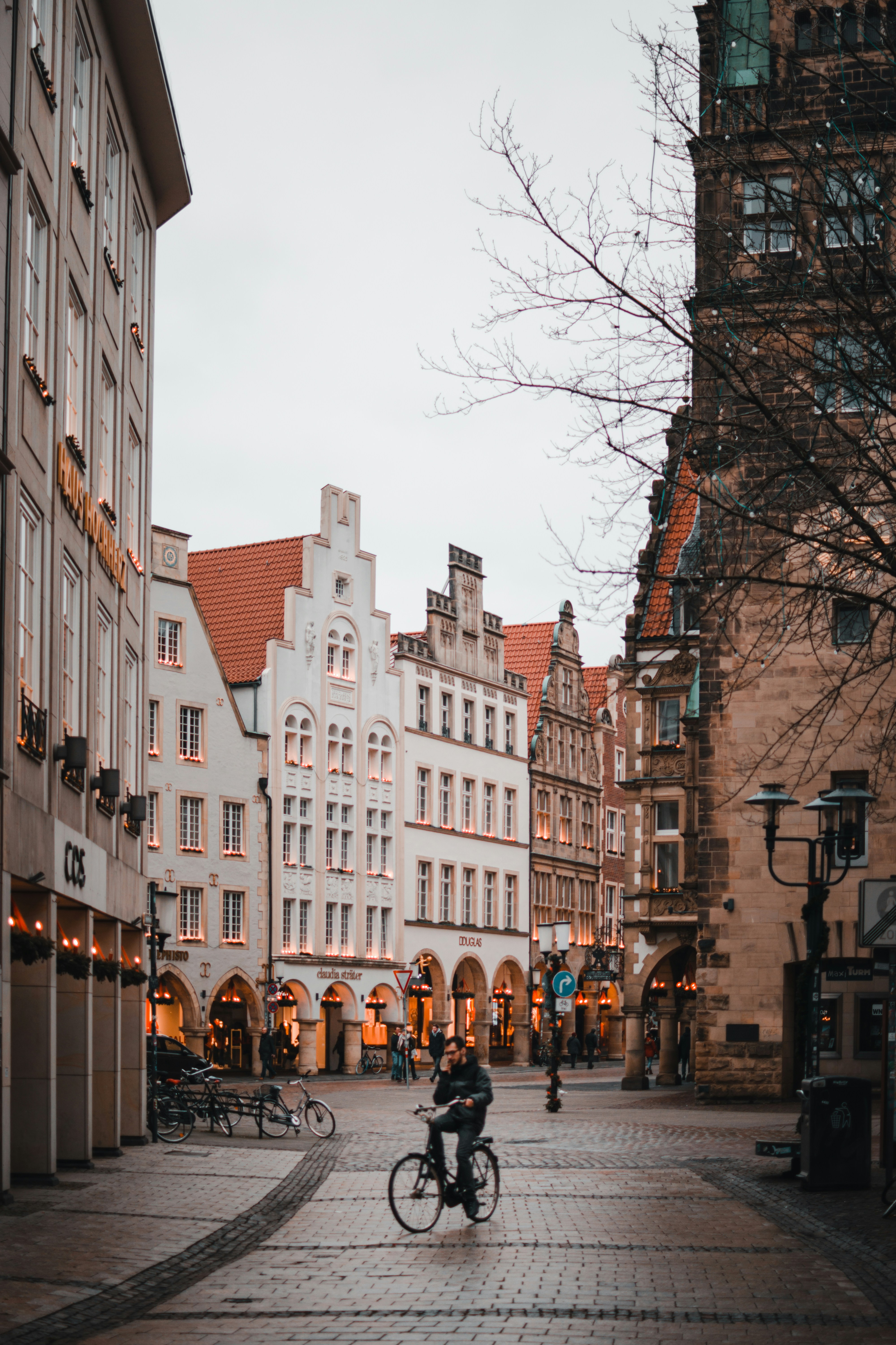 Cyclist navigating through a charming European street lined with historic architecture and subtle evening lights.