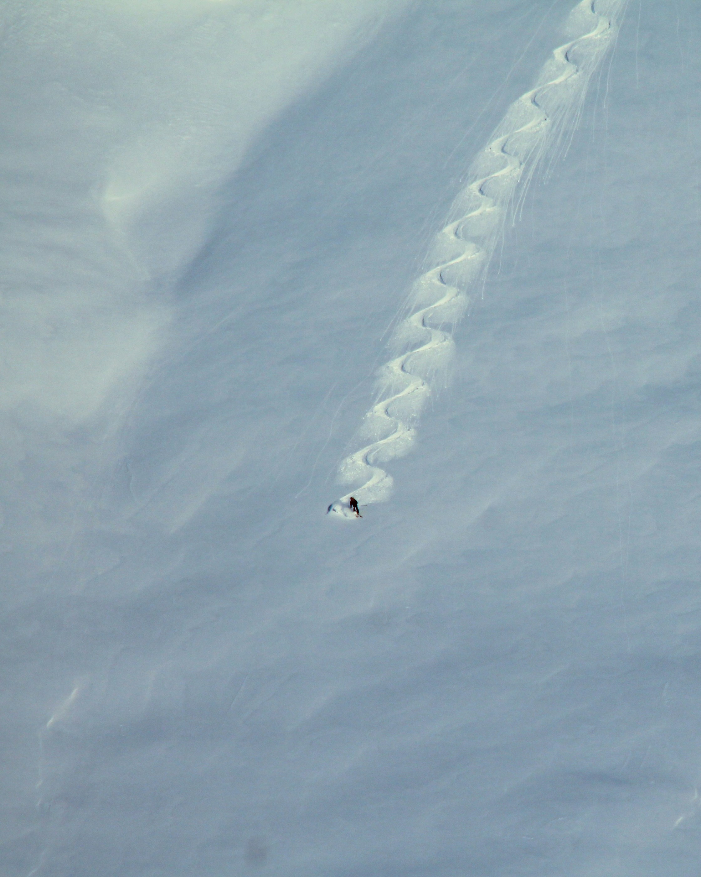Lone Skier Tracing a Curved Wake on a Pale Alpine Slope