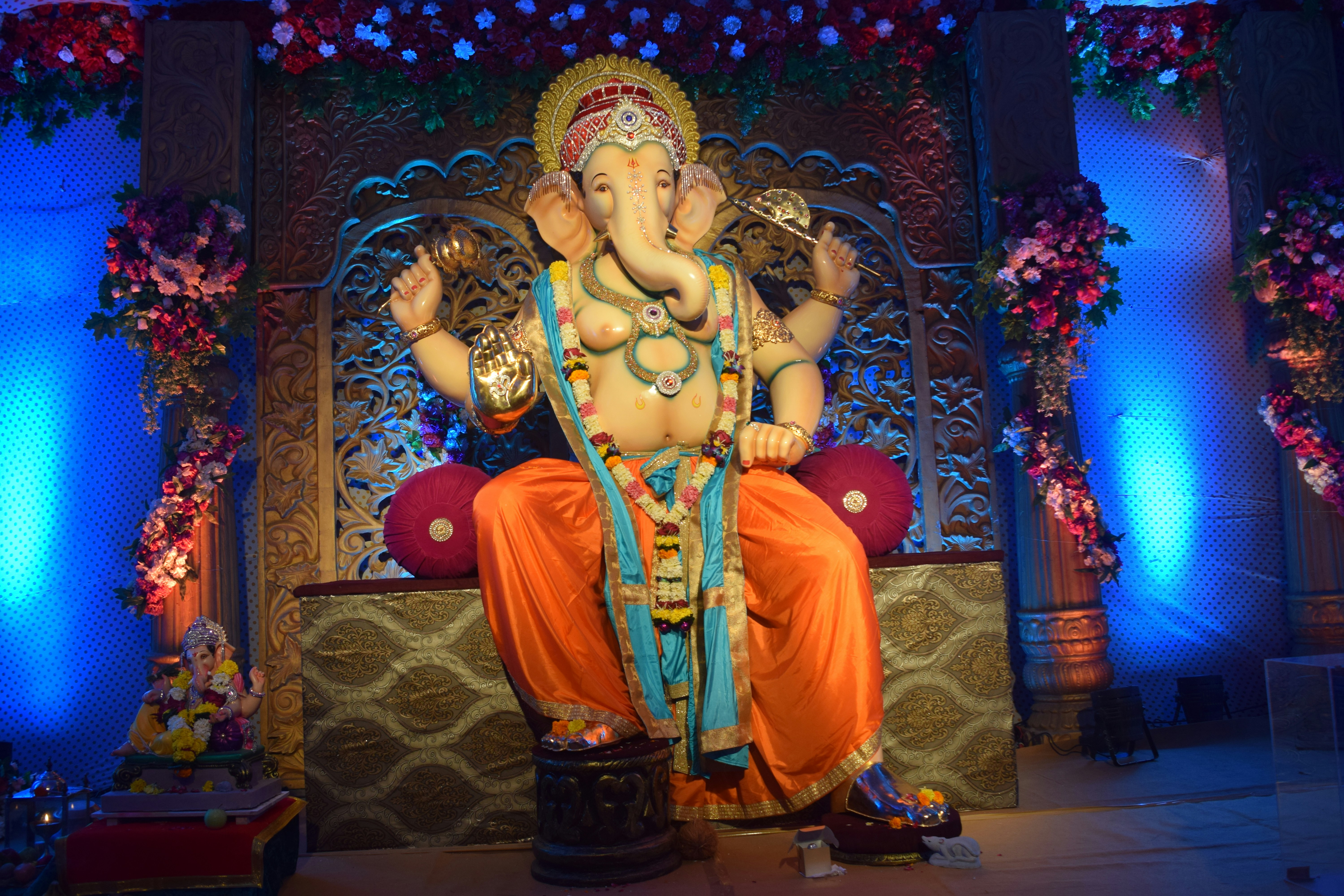 Vibrant idol of Lord Ganesha adorned with intricate decorations, seated against a backdrop of colorful floral arrangements and soft lighting.