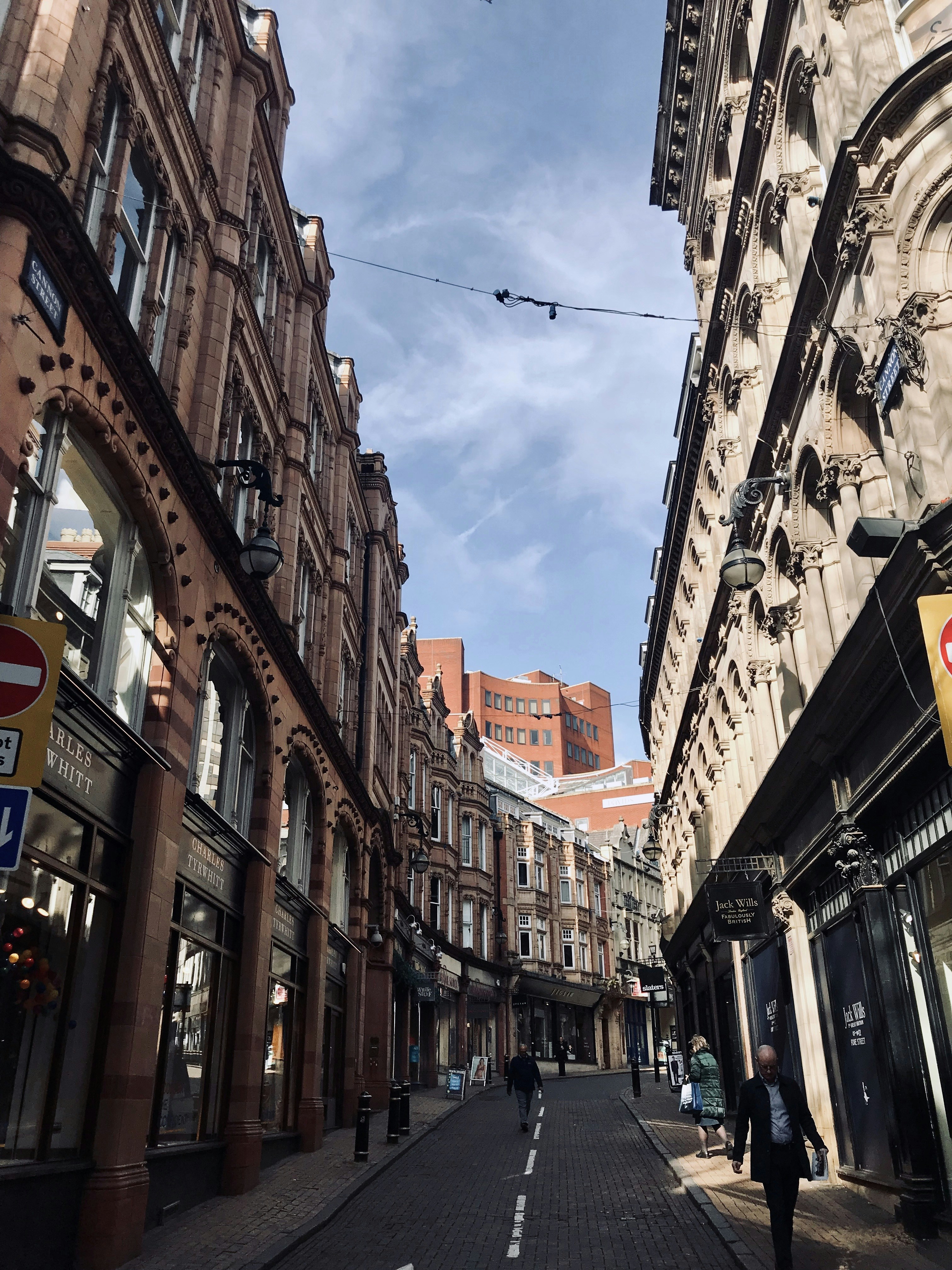 Historic buildings line a narrow street, bathed in soft daylight, showcasing intricate architectural details and a hint of modernity in the background.