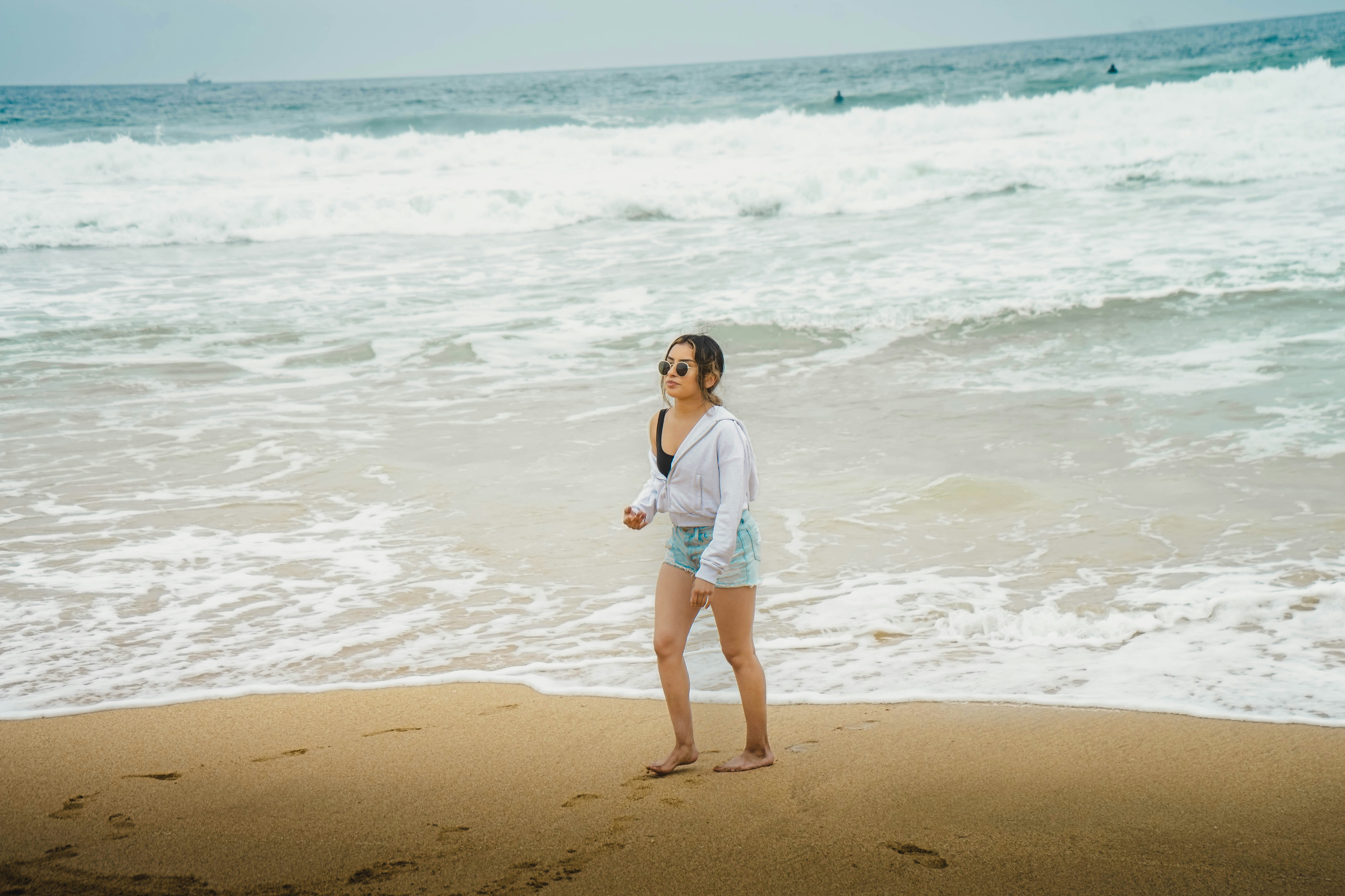 Woman in casual beach attire enjoying the shoreline as waves crash gently around her.