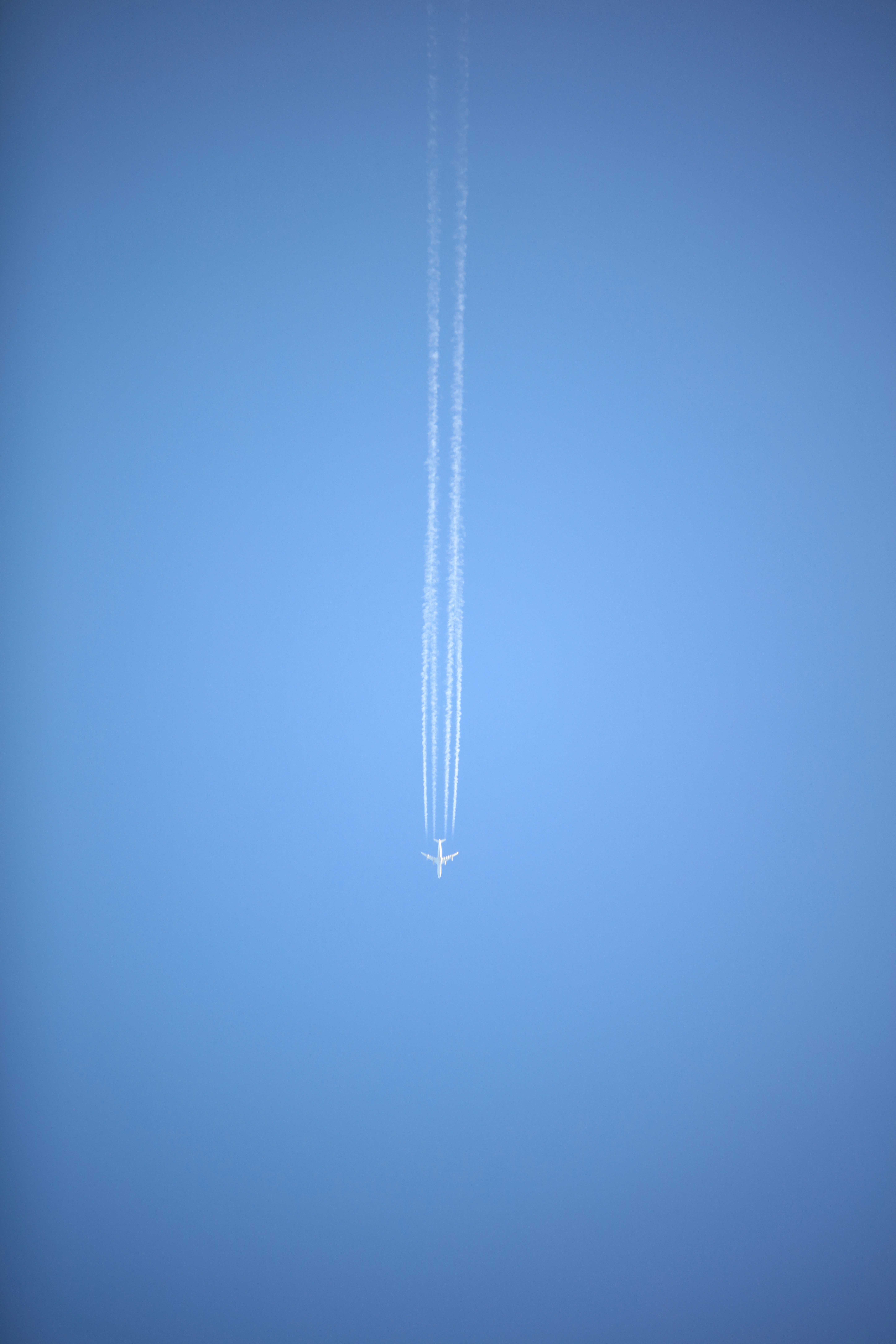 Airplane leaving a vapor trail against a clear blue sky, symbolizing travel and freedom.