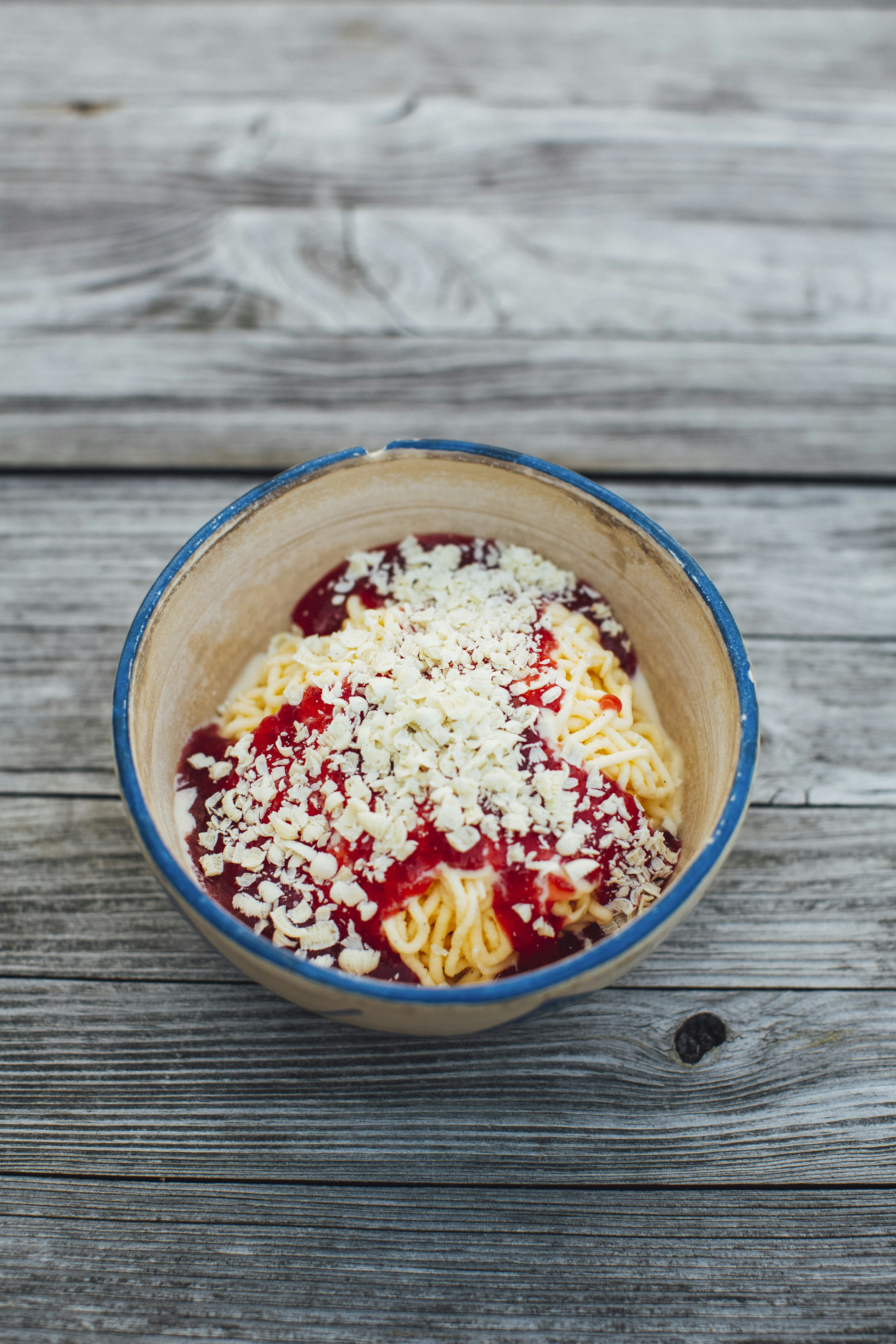 Bowl filled with spaghetti topped with vibrant red sauce and sprinkled with white cheese on a rustic wooden surface.