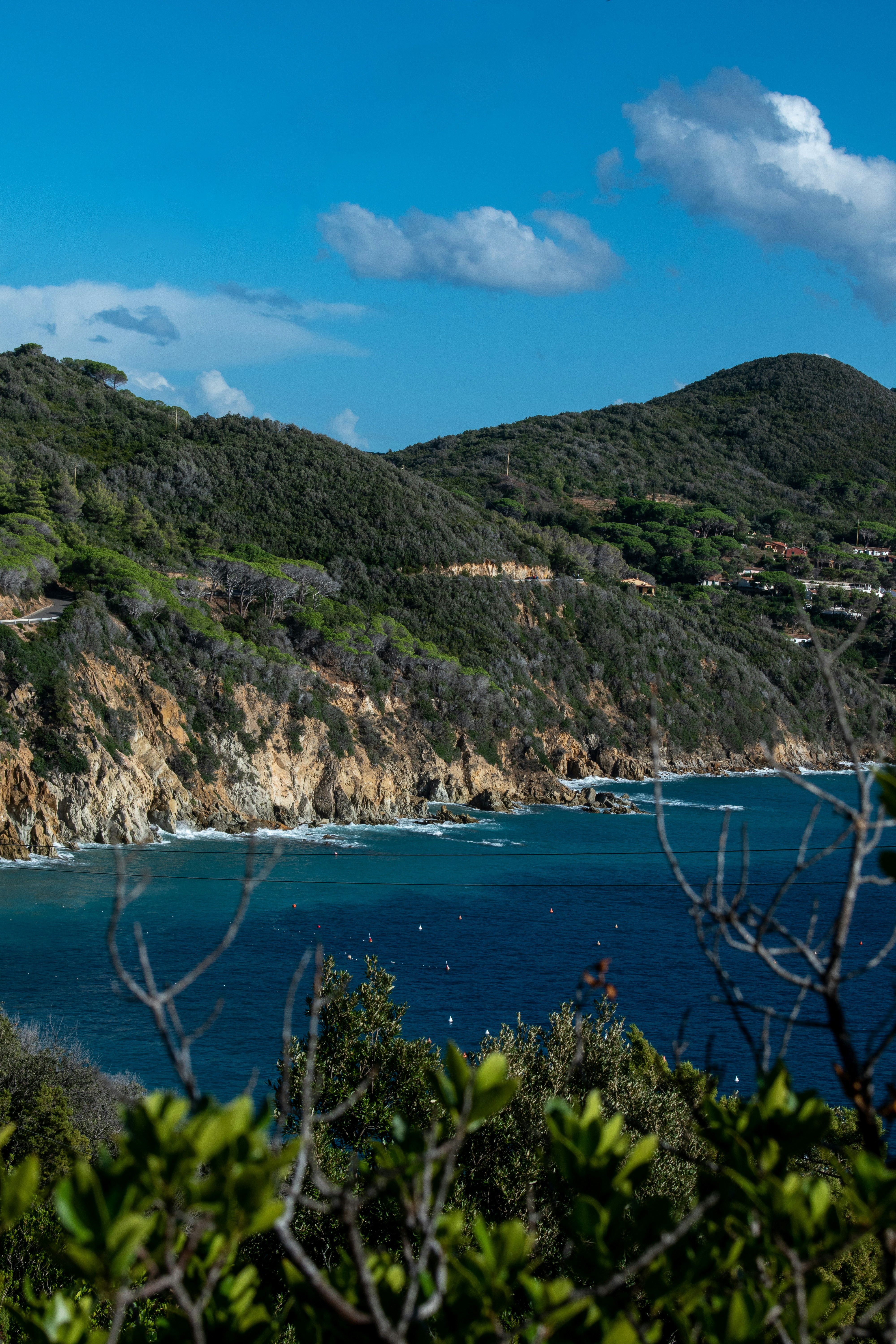 Lush coastal landscape featuring rugged cliffs and a tranquil sea, dotted with small boats. The scene captures the harmony between land and water.