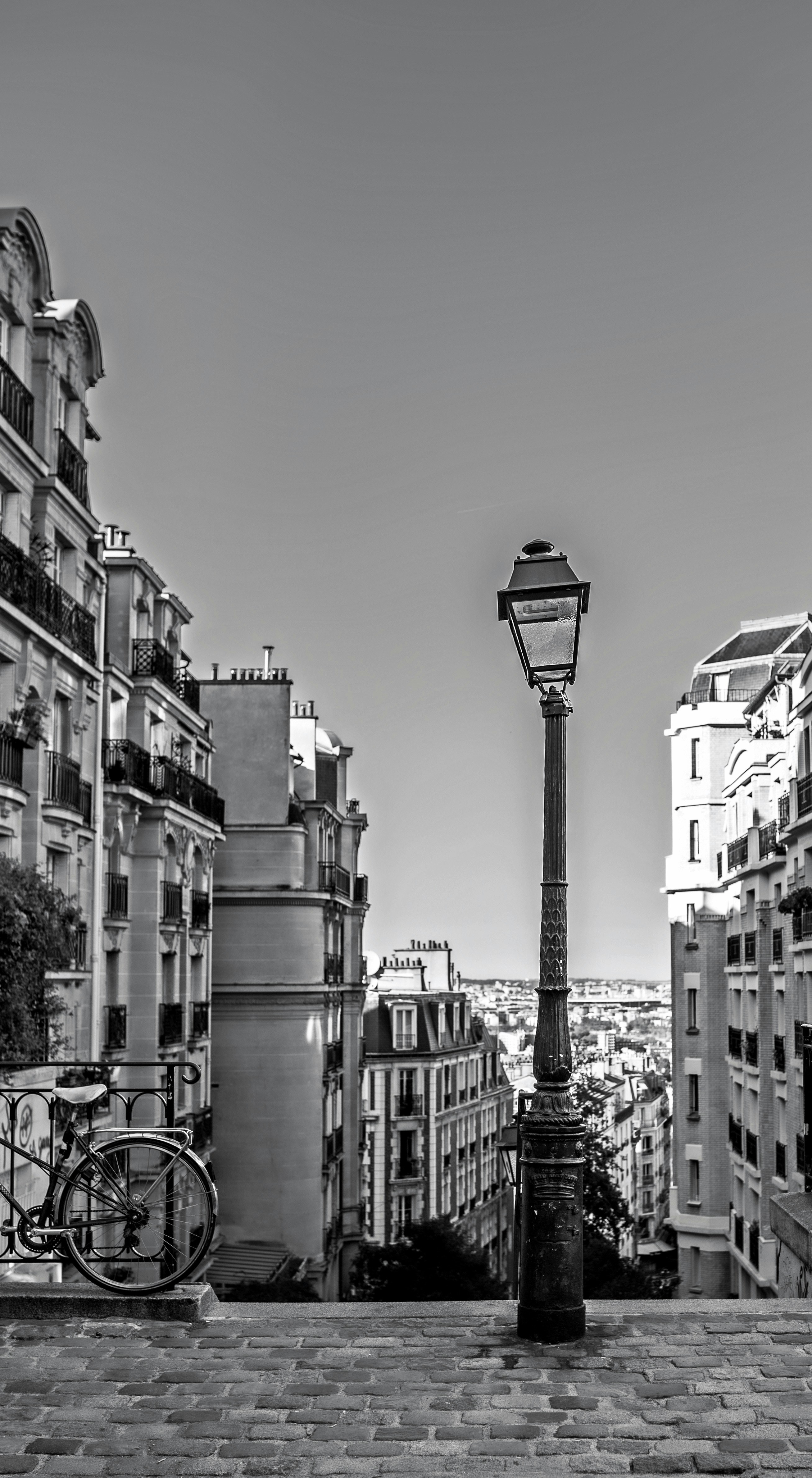 Black and white street view with a central lamppost flanked by classic Parisian buildings and a bicycle.