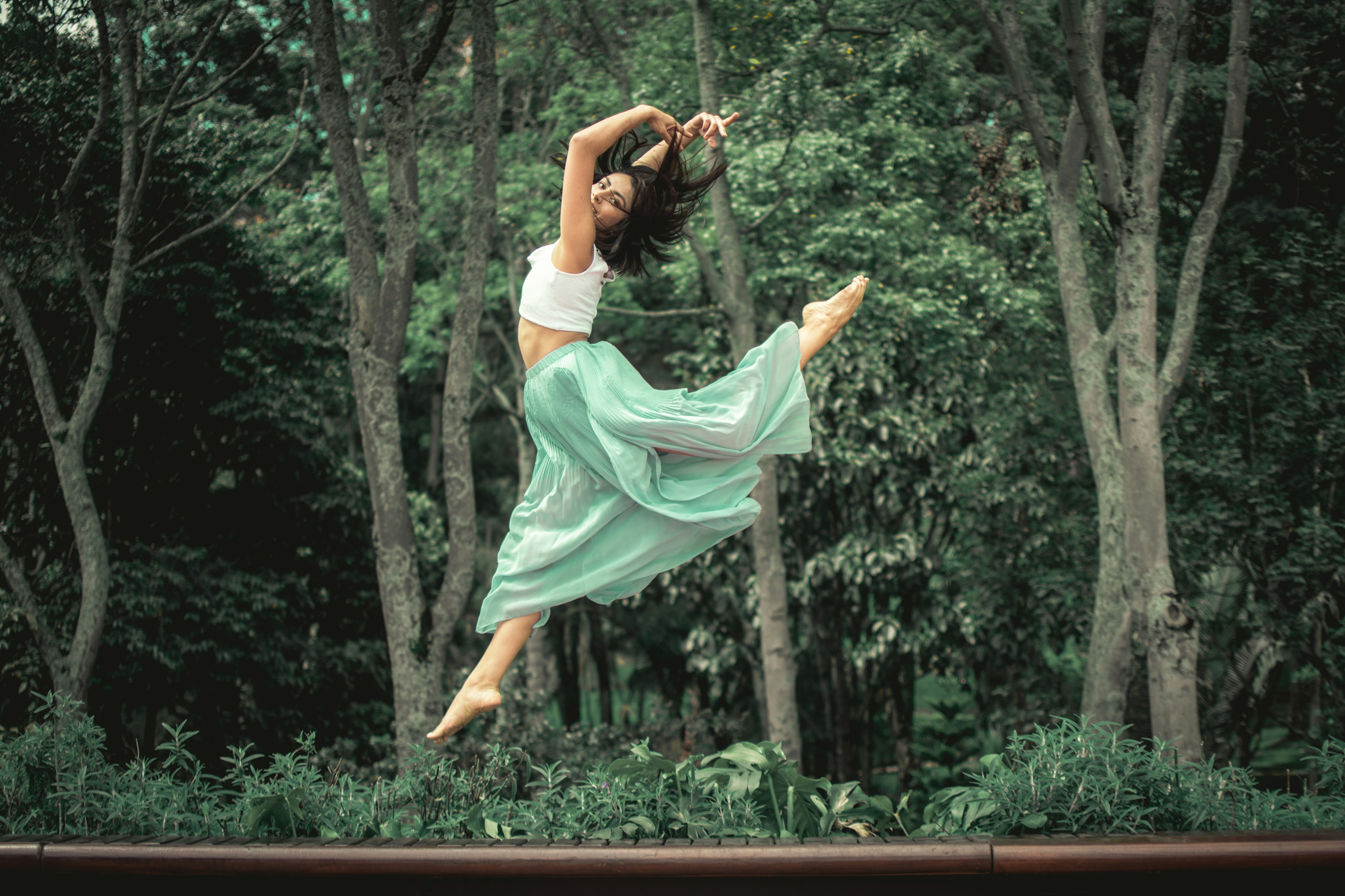 Dancer in a flowing green skirt mid-jump against a backdrop of lush forest.