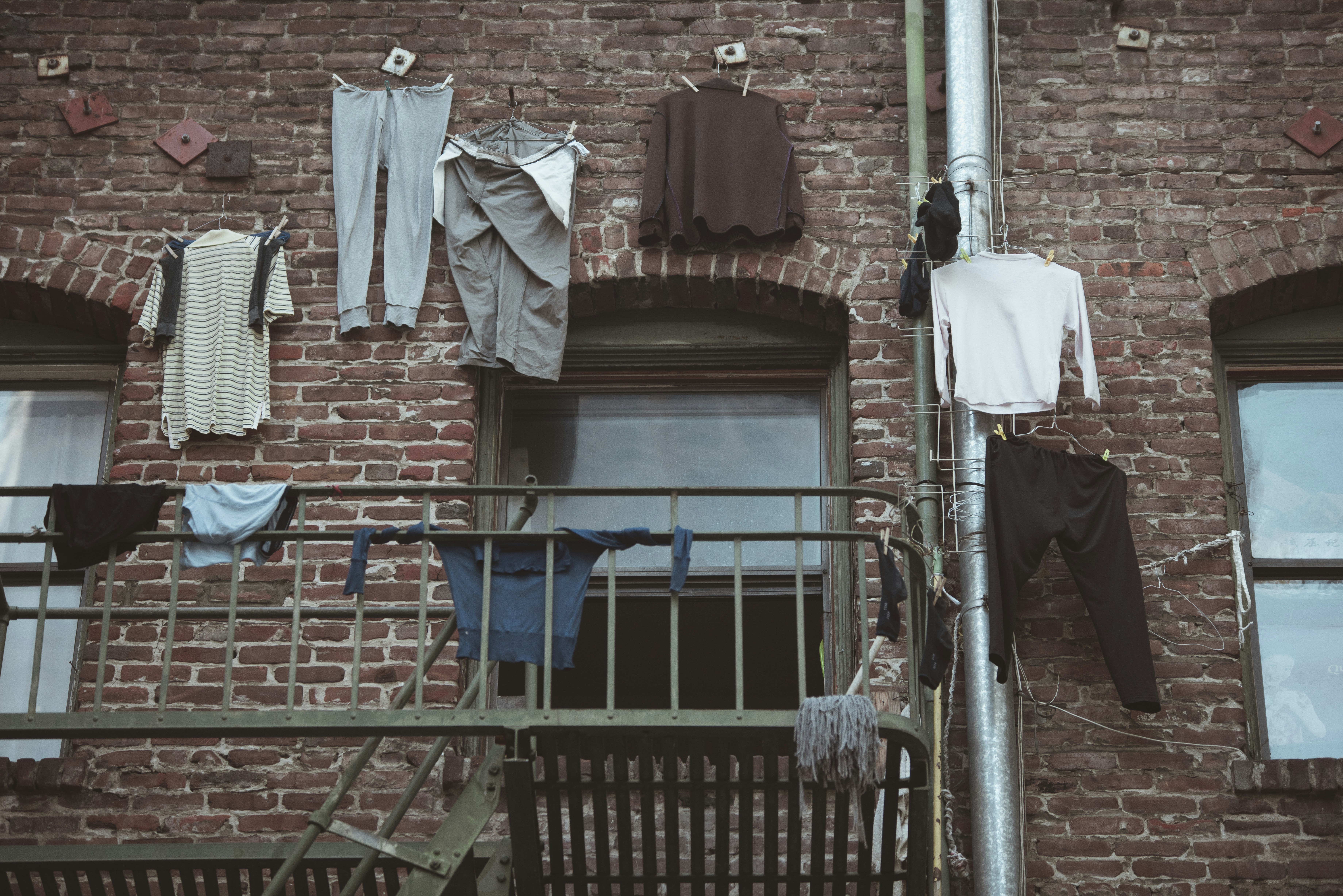 Clothing hangs on a fire escape and brick wall of an urban building, creating a makeshift clothesline.