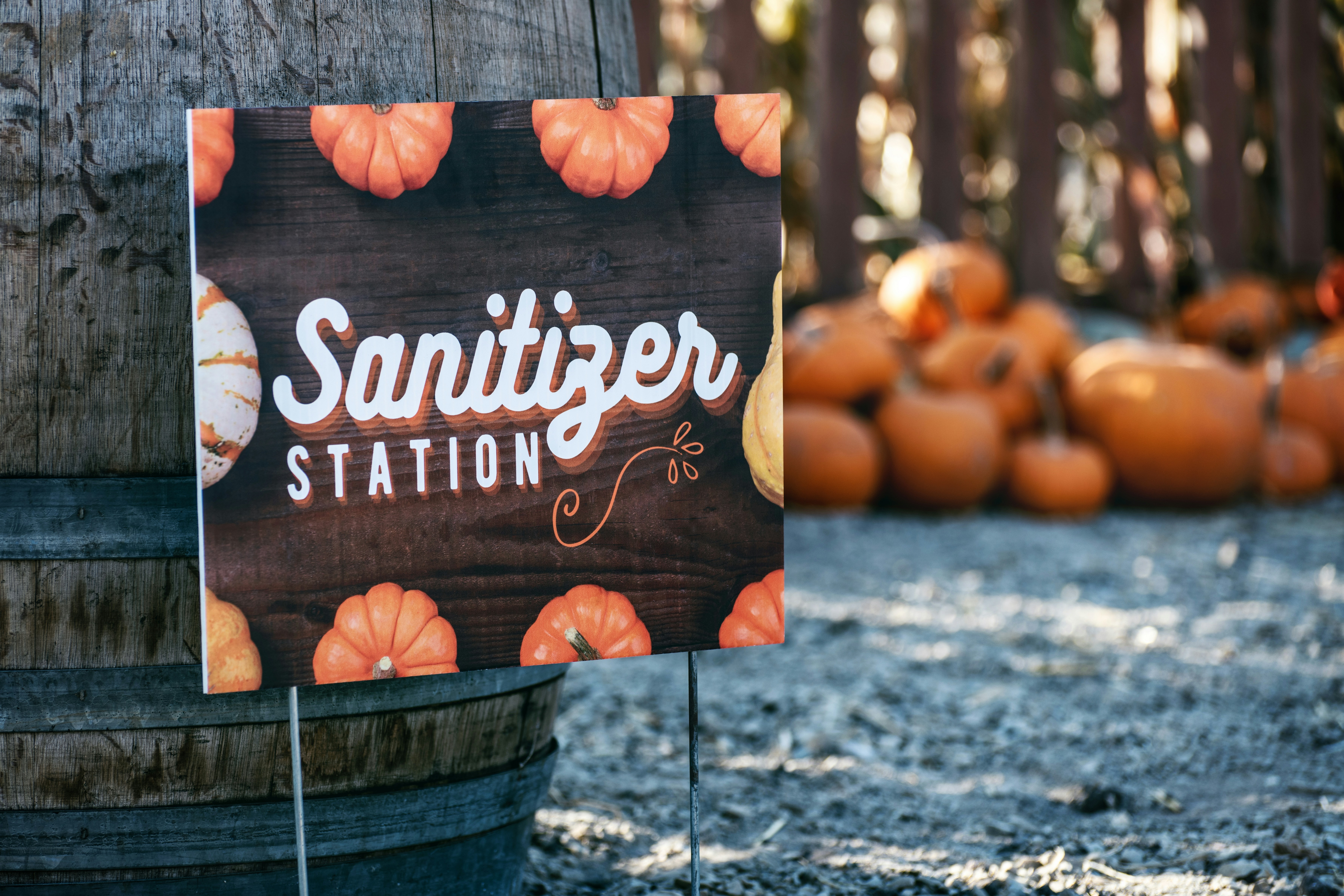 Sign indicating a sanitizer station, adorned with pumpkins, set against a rustic barrel backdrop.