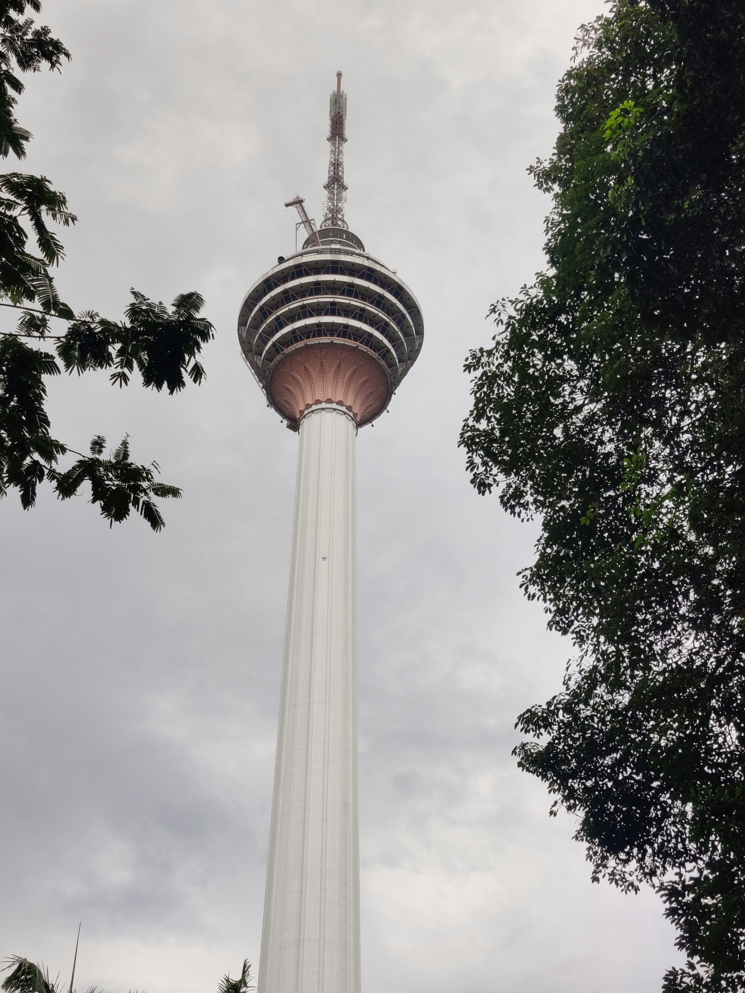 A towering telecommunications structure rises against a cloudy sky, framed by lush greenery. The design showcases modern architecture and engineering prowess.