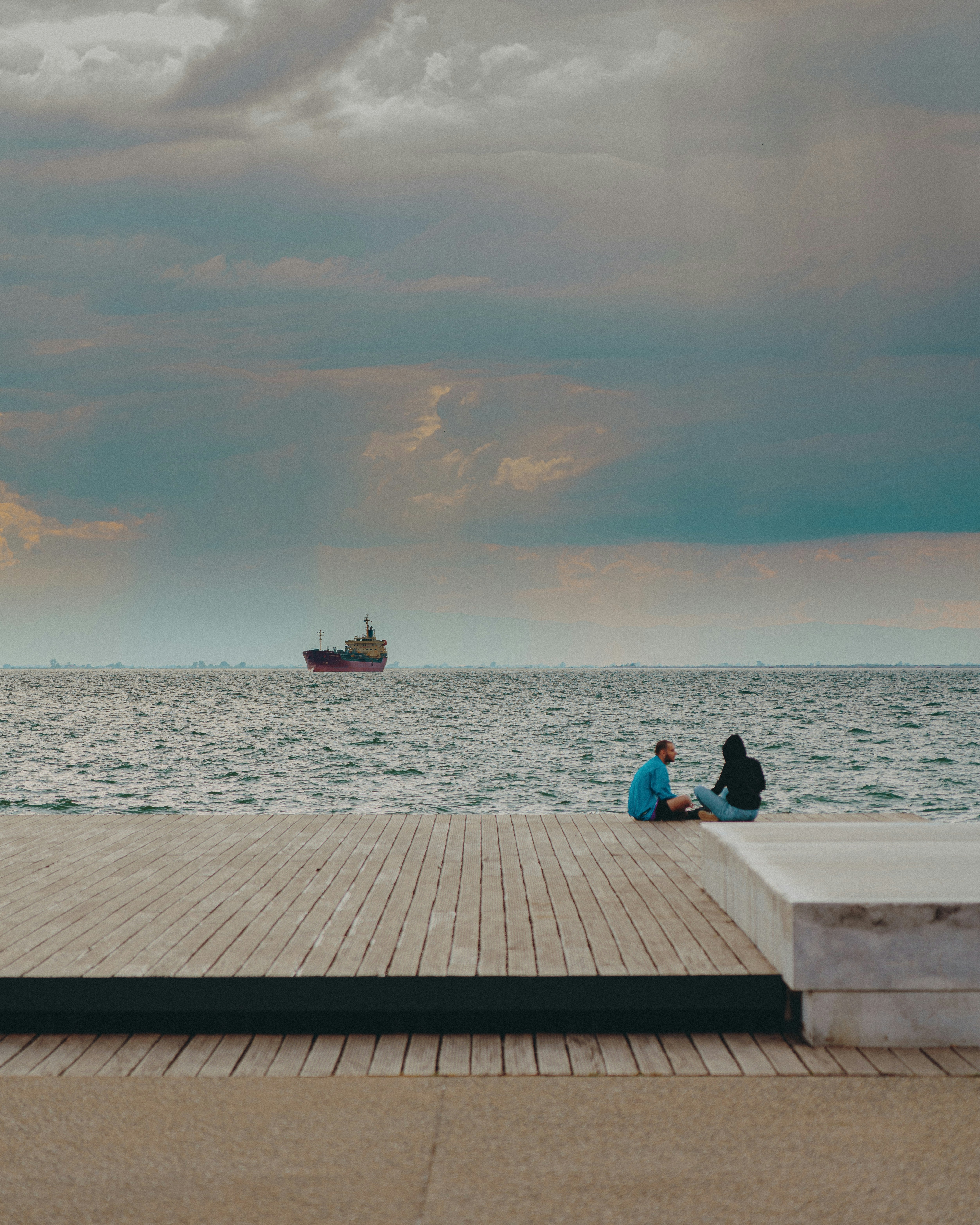 Pierside Calm: Conversation by the Sea as a Cargo Ship Crosses the Horizon