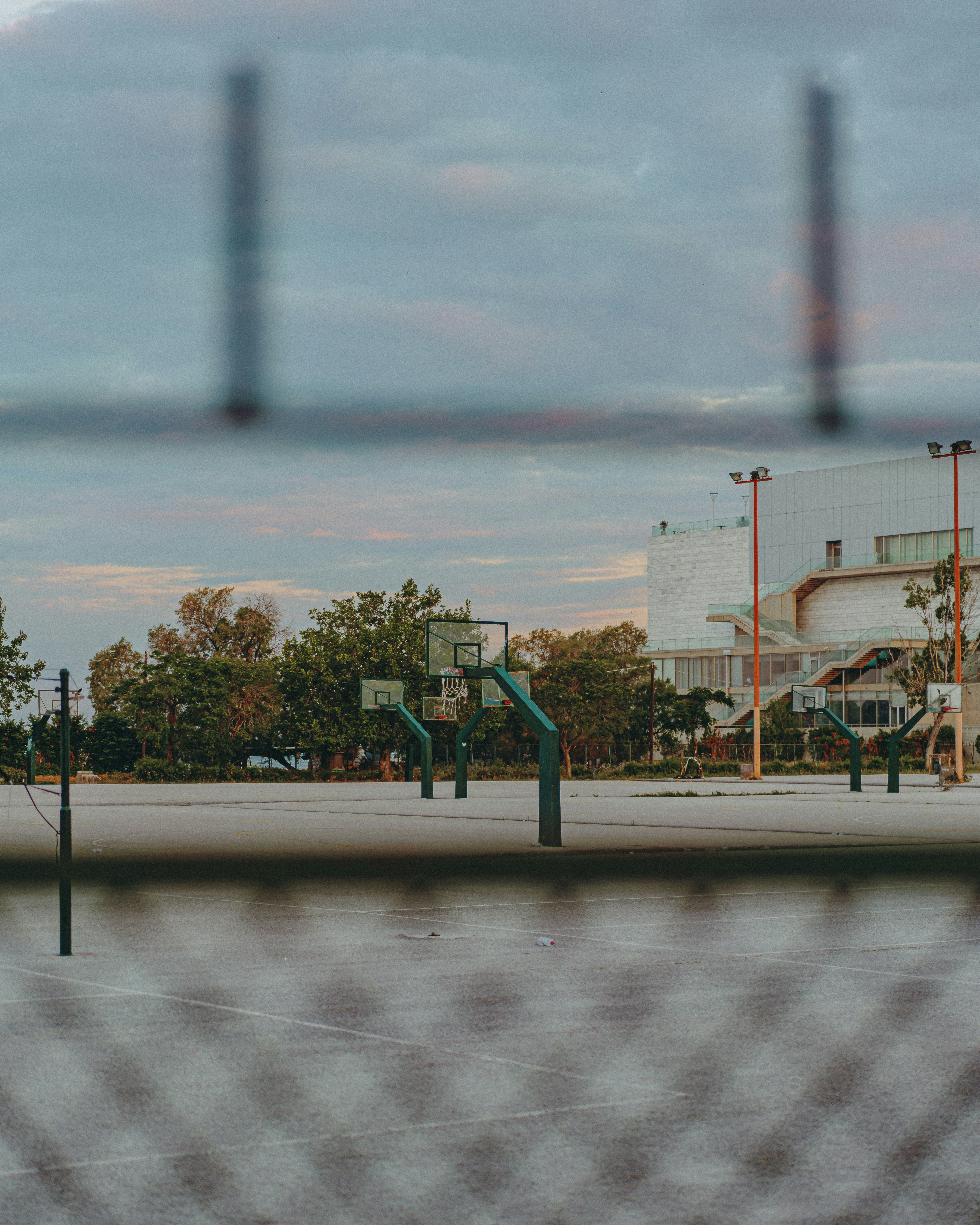 Fence-Frame Court: Green Hoops and a Distant Building under Quiet Evening Light