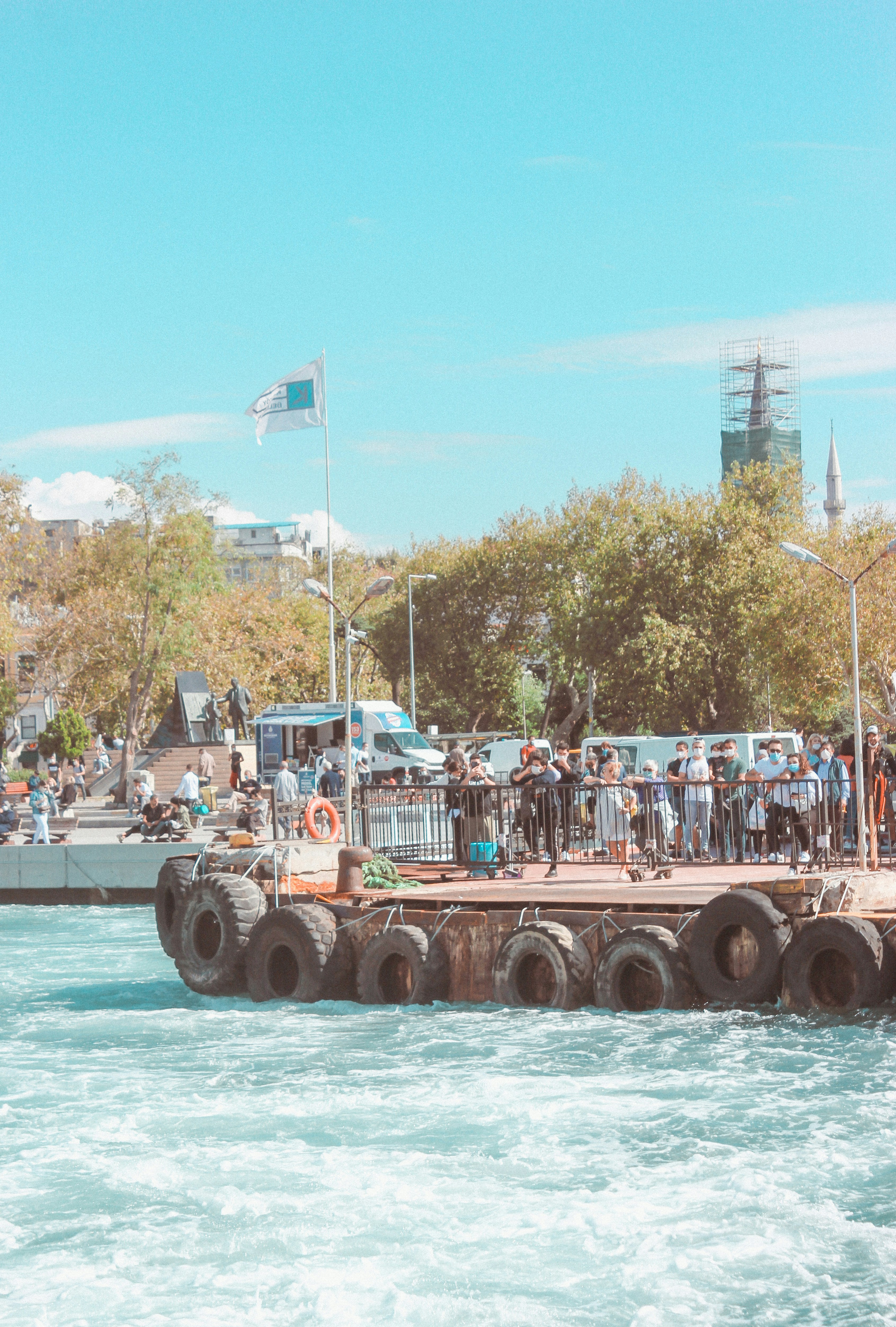 Tire-Dotted Dockside Crowd Beneath a Sunlit Riverfront