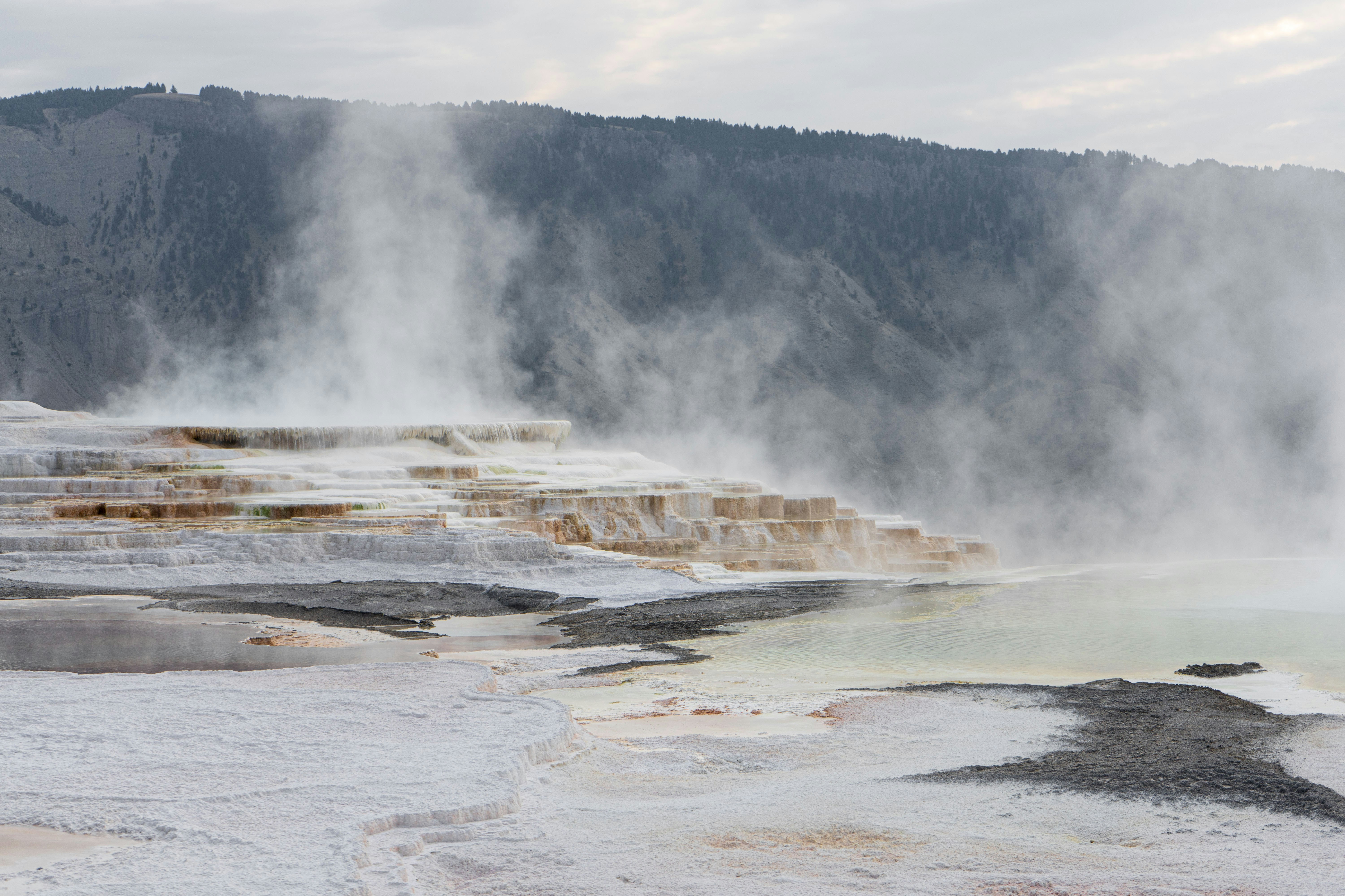 Geothermal terraces emitting steam against a backdrop of rugged mountains.