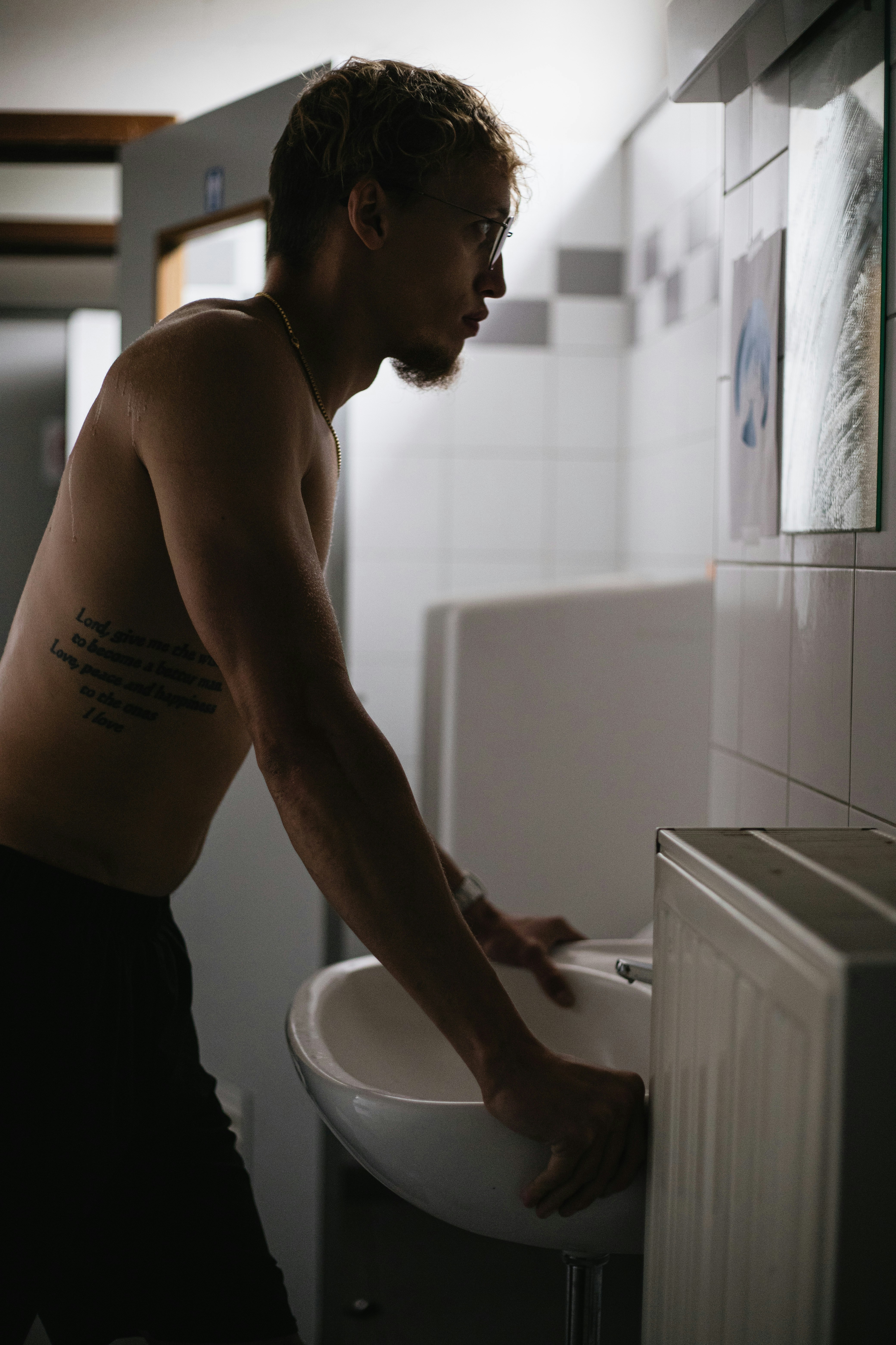 Portrait with Sink: A Shirtless Moment of Reflection in a Dim Locker-Like Room