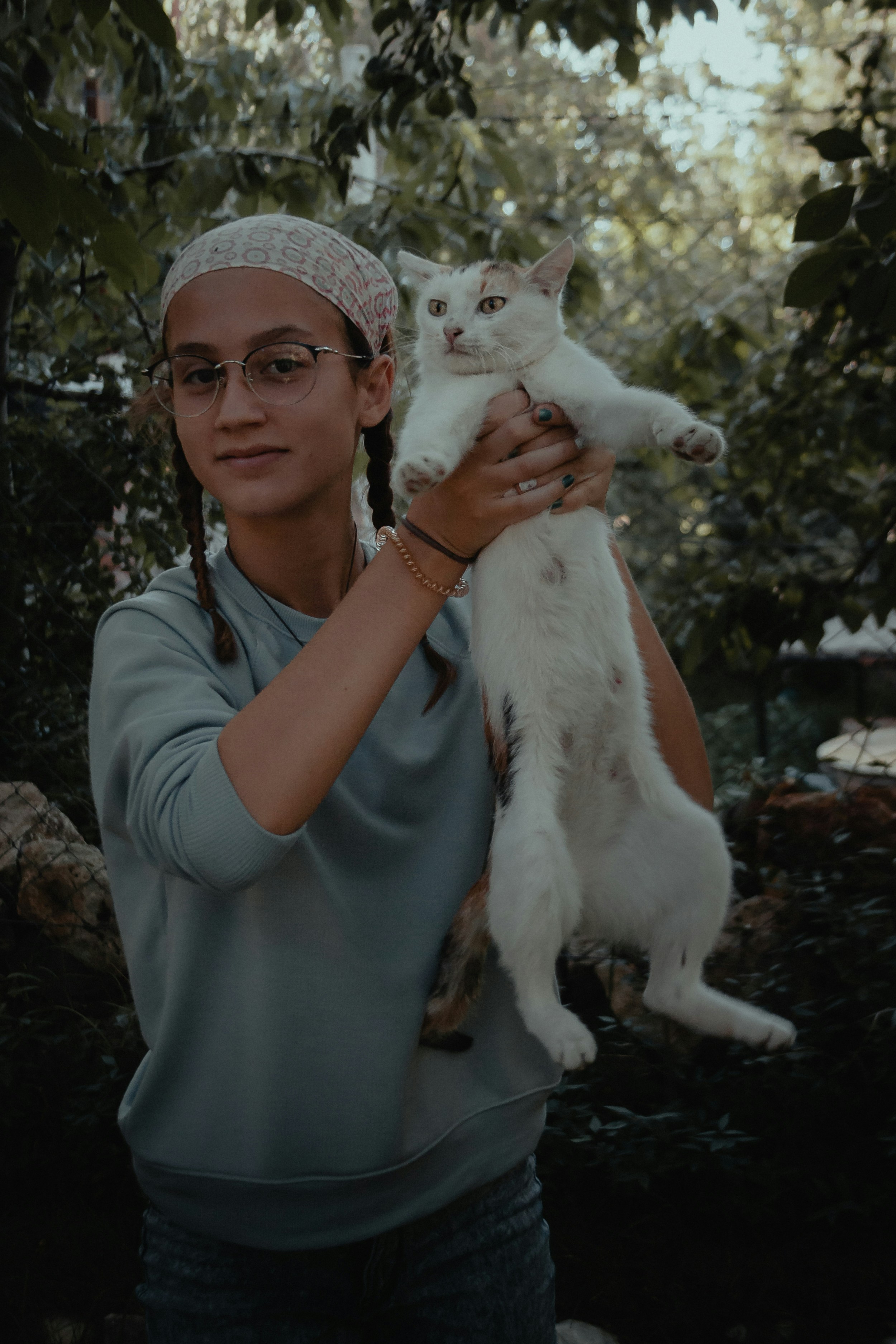 Dappled Light, Quiet Bond: A Girl Lifts Her White Cat in a Garden